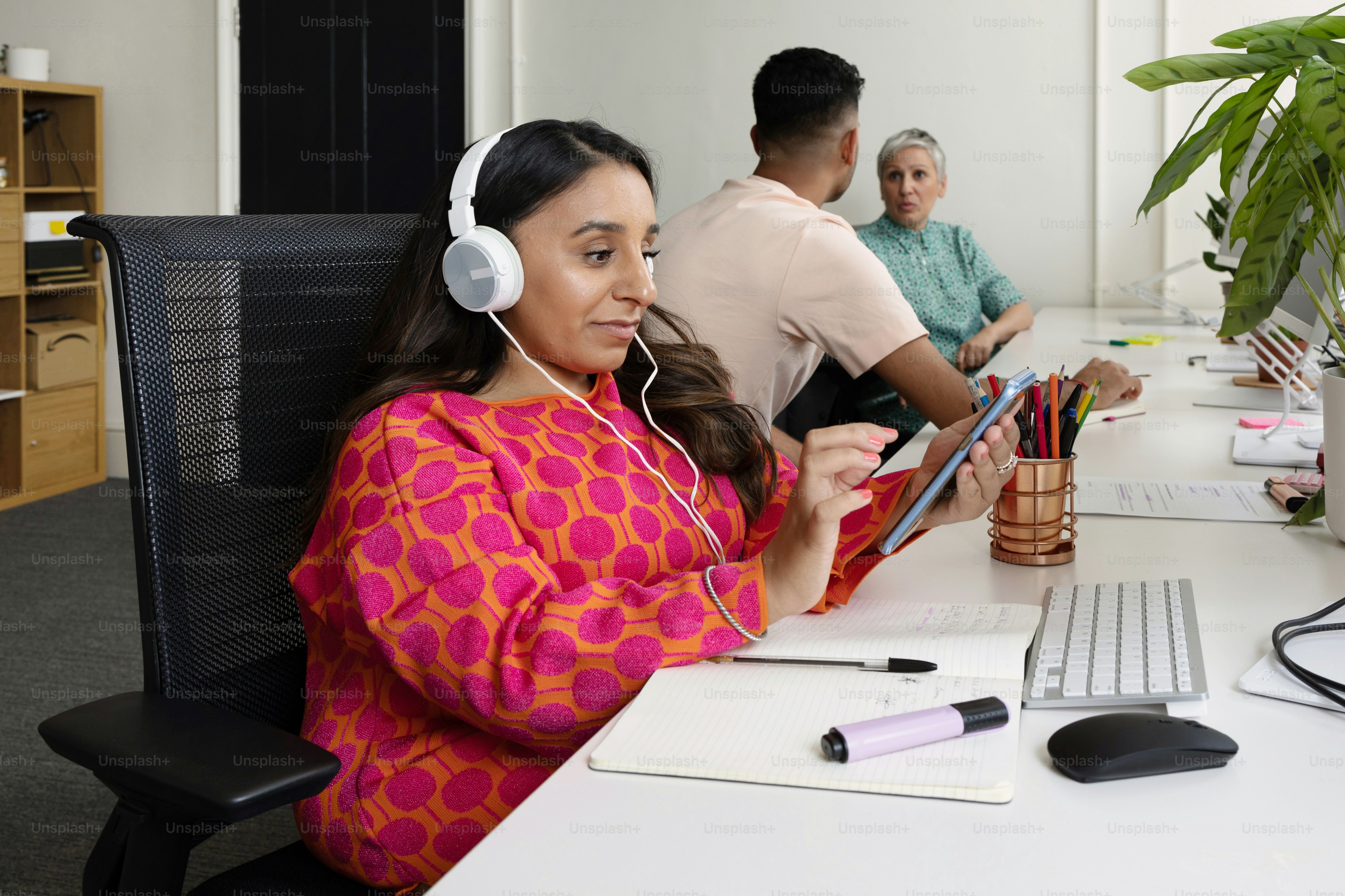 A woman sitting at a desk with headphones on photo – Office worker ...