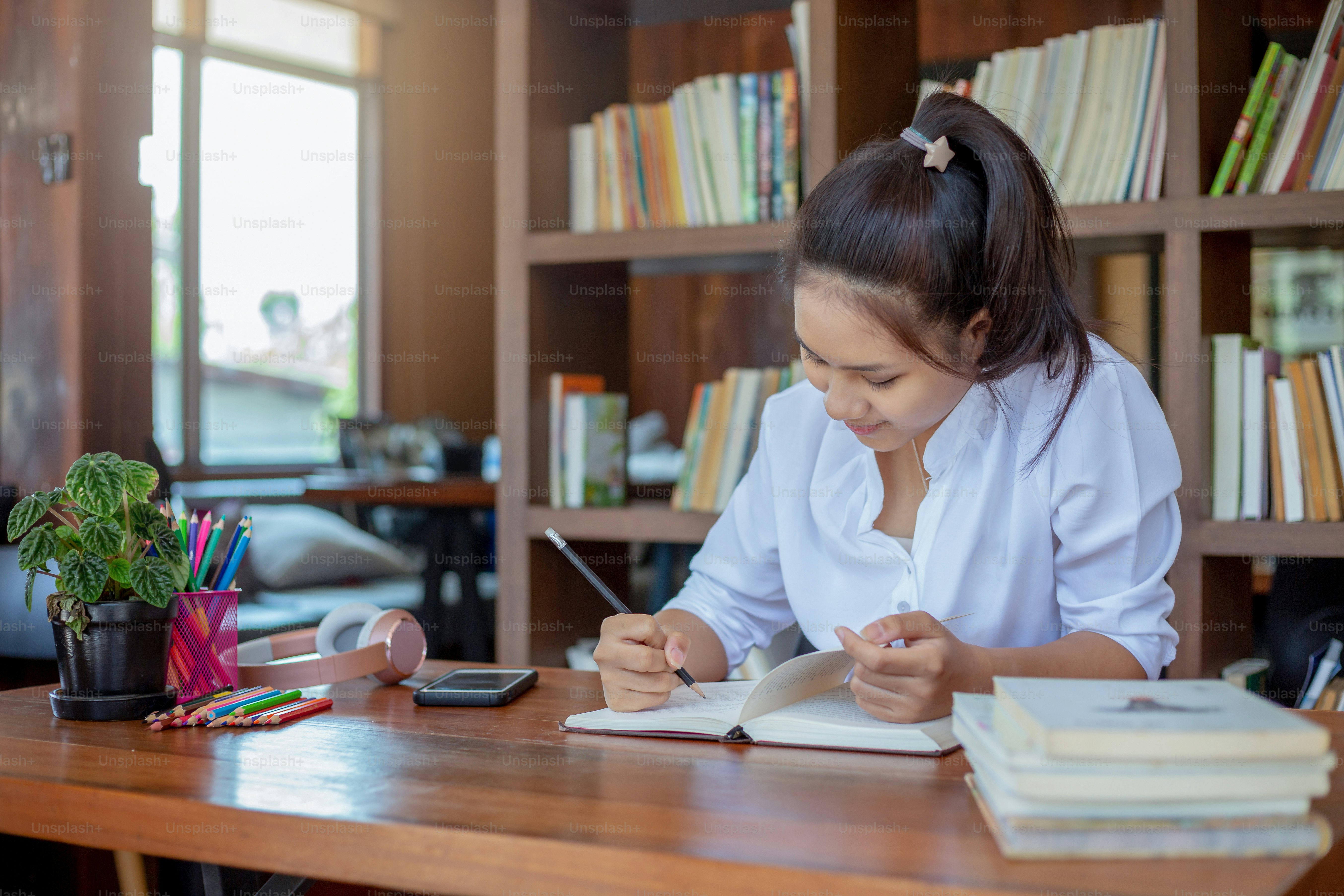 Asian female student sitting and write a note on table library at ...