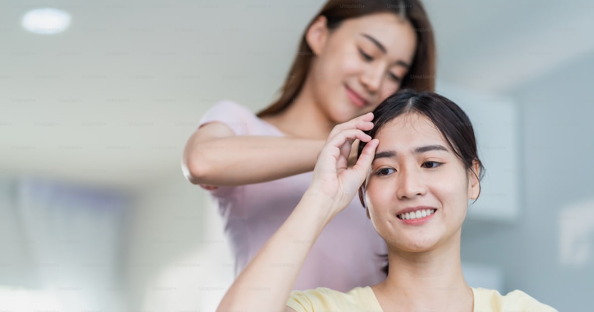 아시아의 아름다운 레즈비언 여성 커플이 집에서 여자 친구 머리를 빗질하고 있다 매력적인 두 여자 게이 친구가 거실의 소파에
