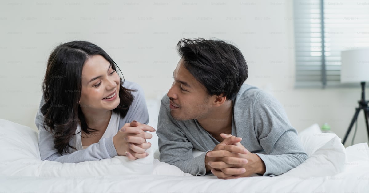 아시아의 새로운 결혼 커플의 초상화는 침대에 누워 서로를 본다 잠옷을 입은 매력적인 아름다운 젊은 남녀가 집에서 침실에서 이른