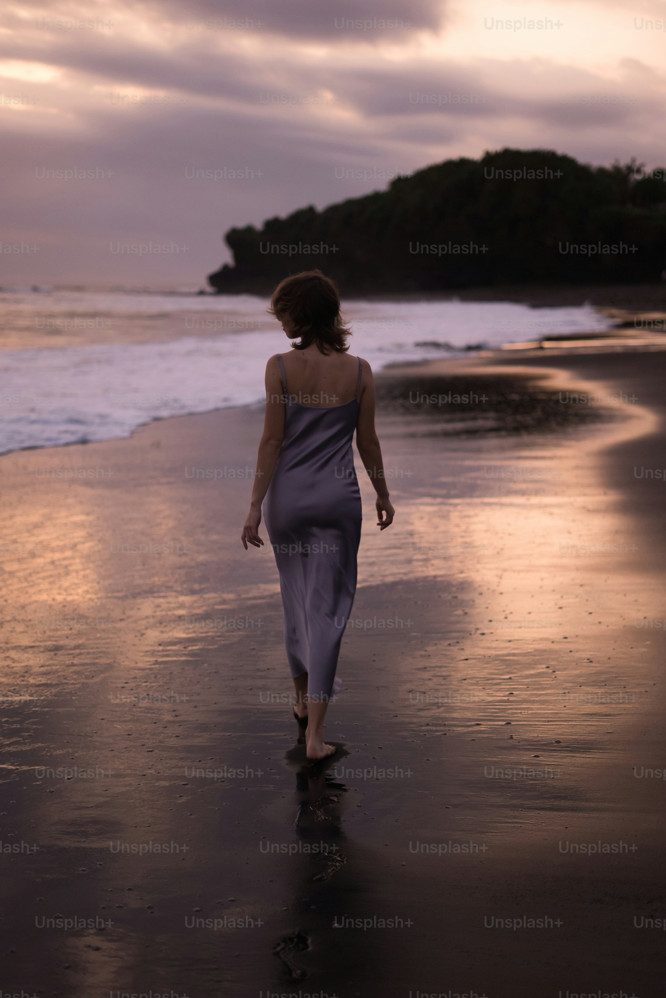 A woman walking along a beach next to the ocean photo – Bali Image on ...