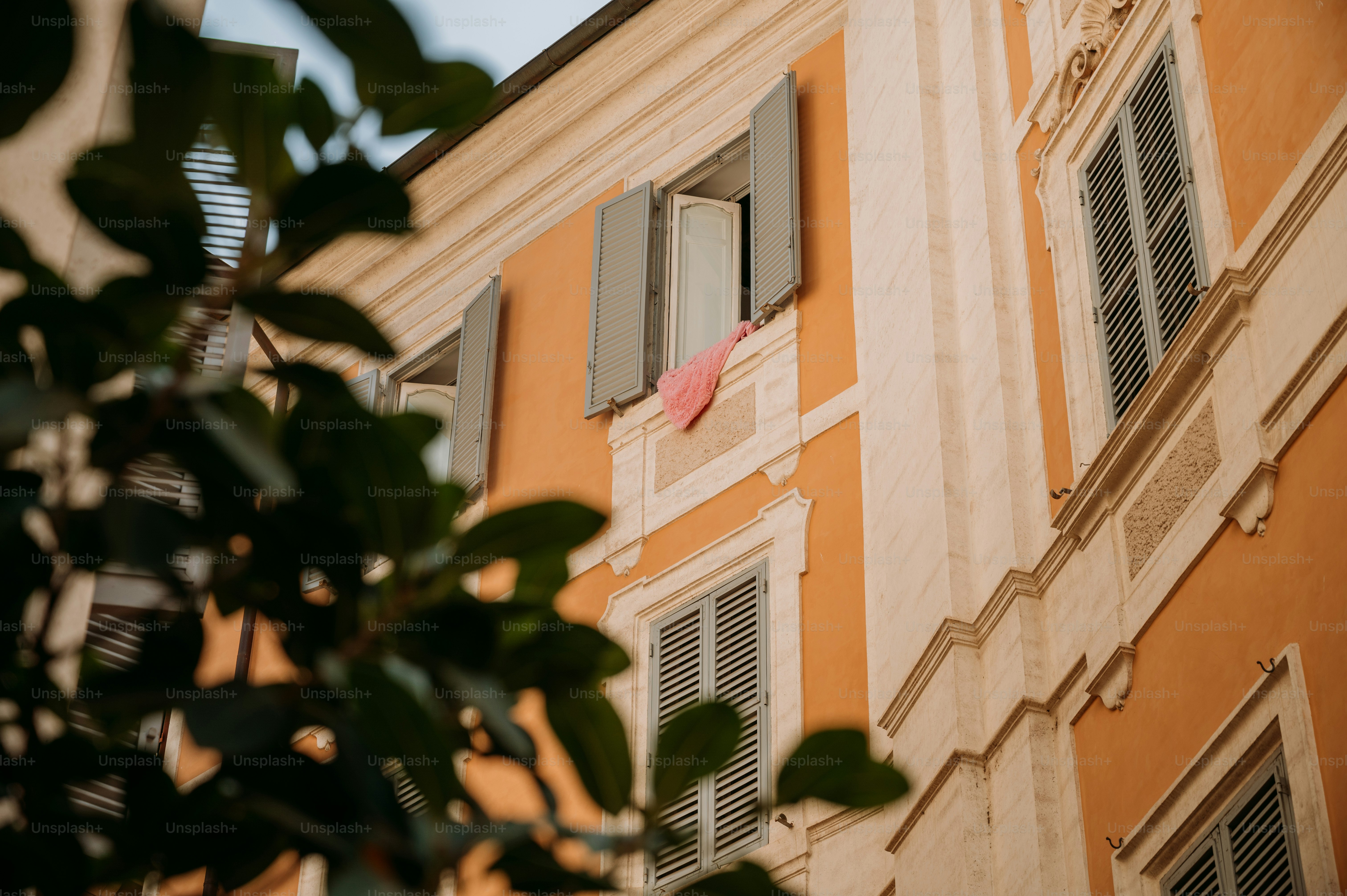 An orange building with shutters and a pink umbrella photo – Italy ...