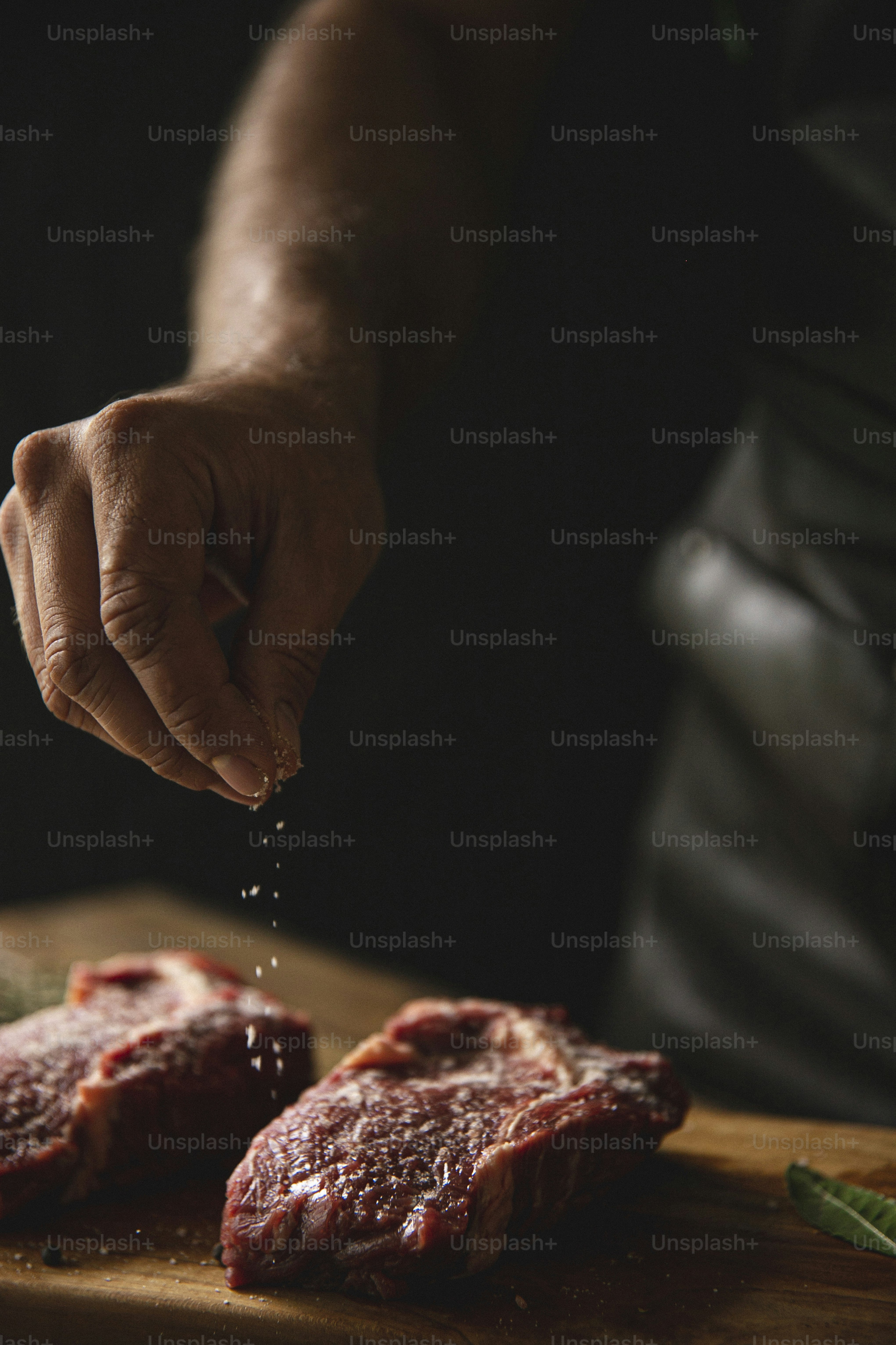 A person sprinkling seasoning on a piece of meat photo – Beef joint ...