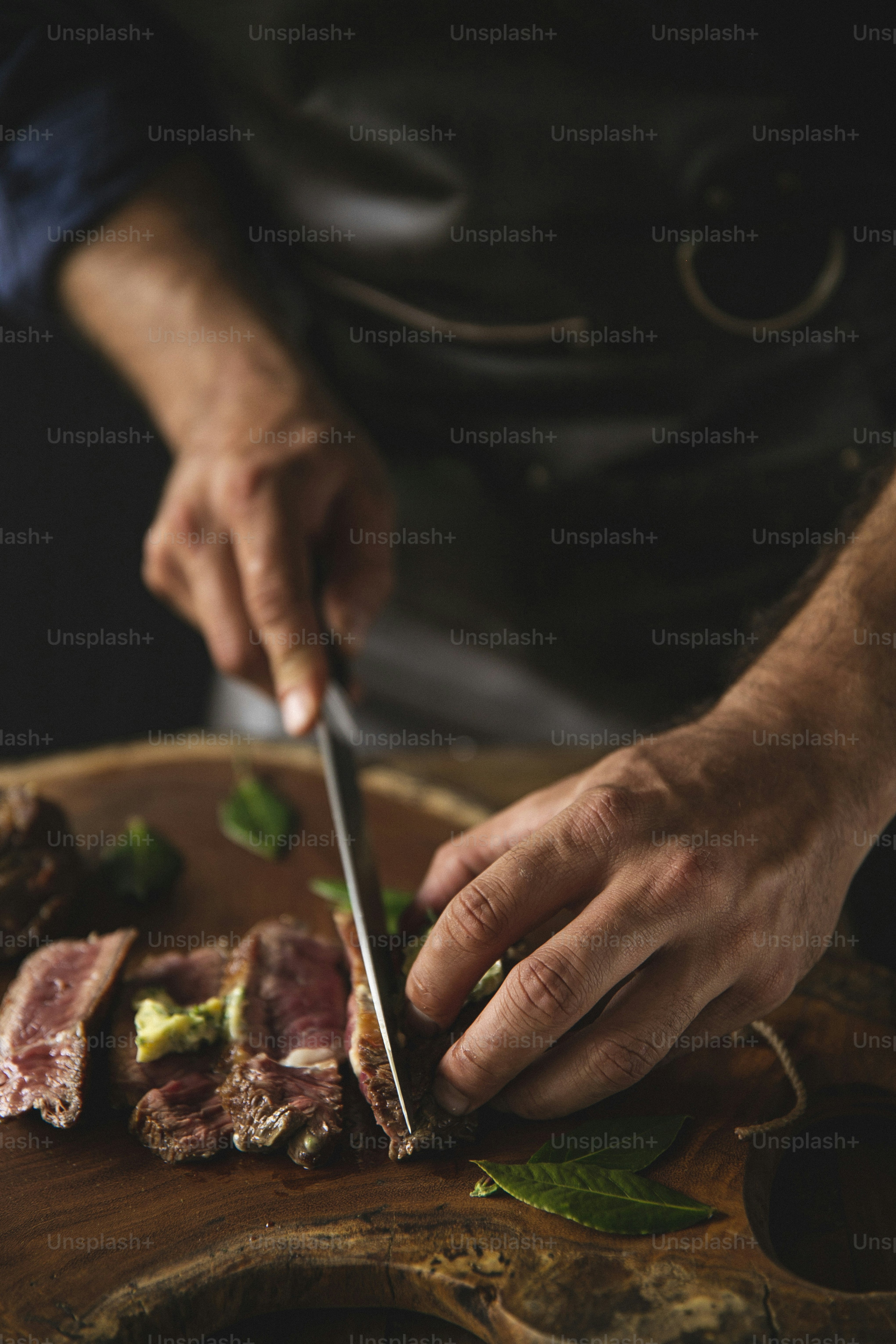 A man cutting up a piece of meat on top of a wooden cutting board photo ...