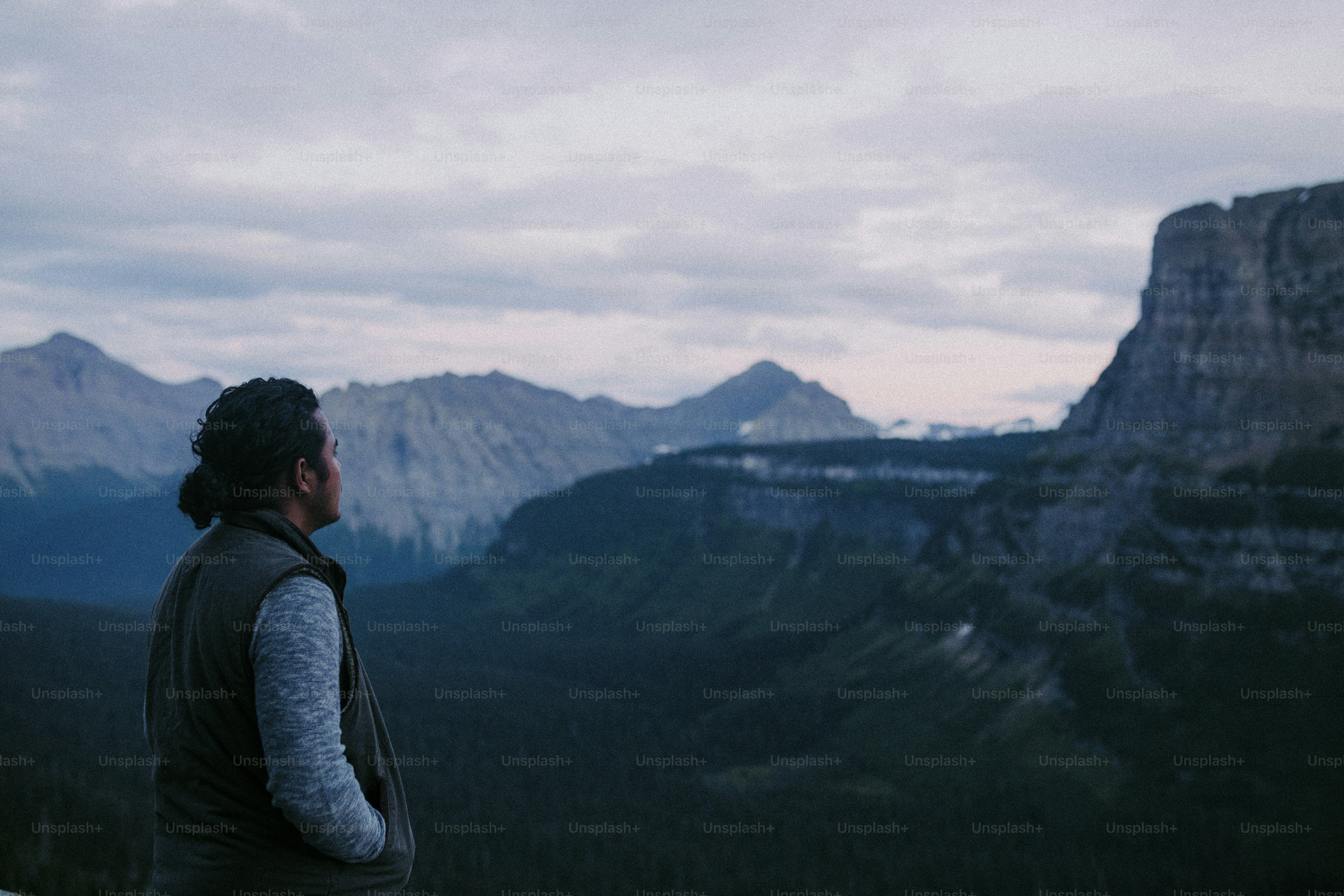 A man standing on top of a mountain overlooking a valley photo – View ...