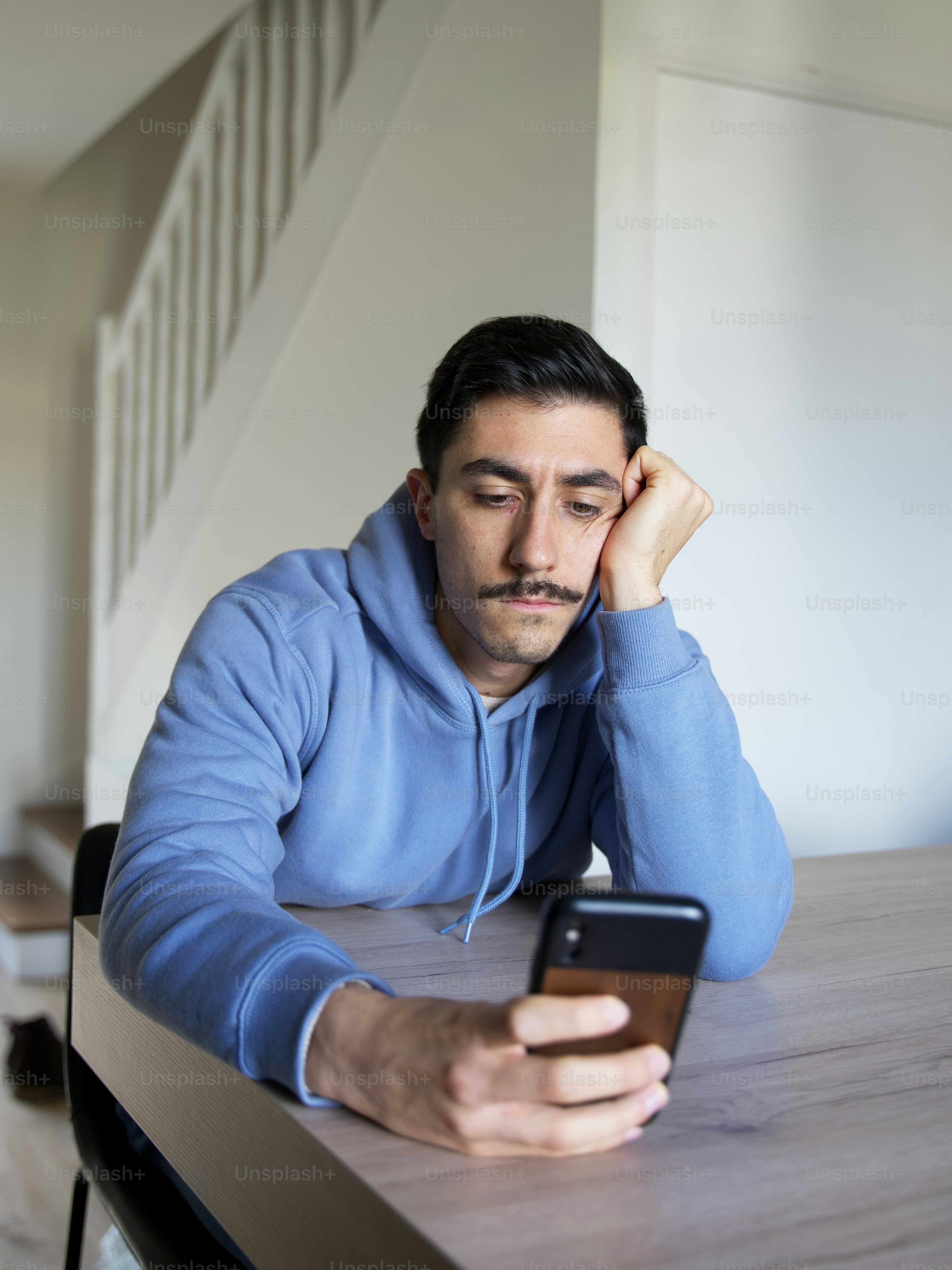 Un homme assis à une table regardant un téléphone photo – Frustré Photo ...