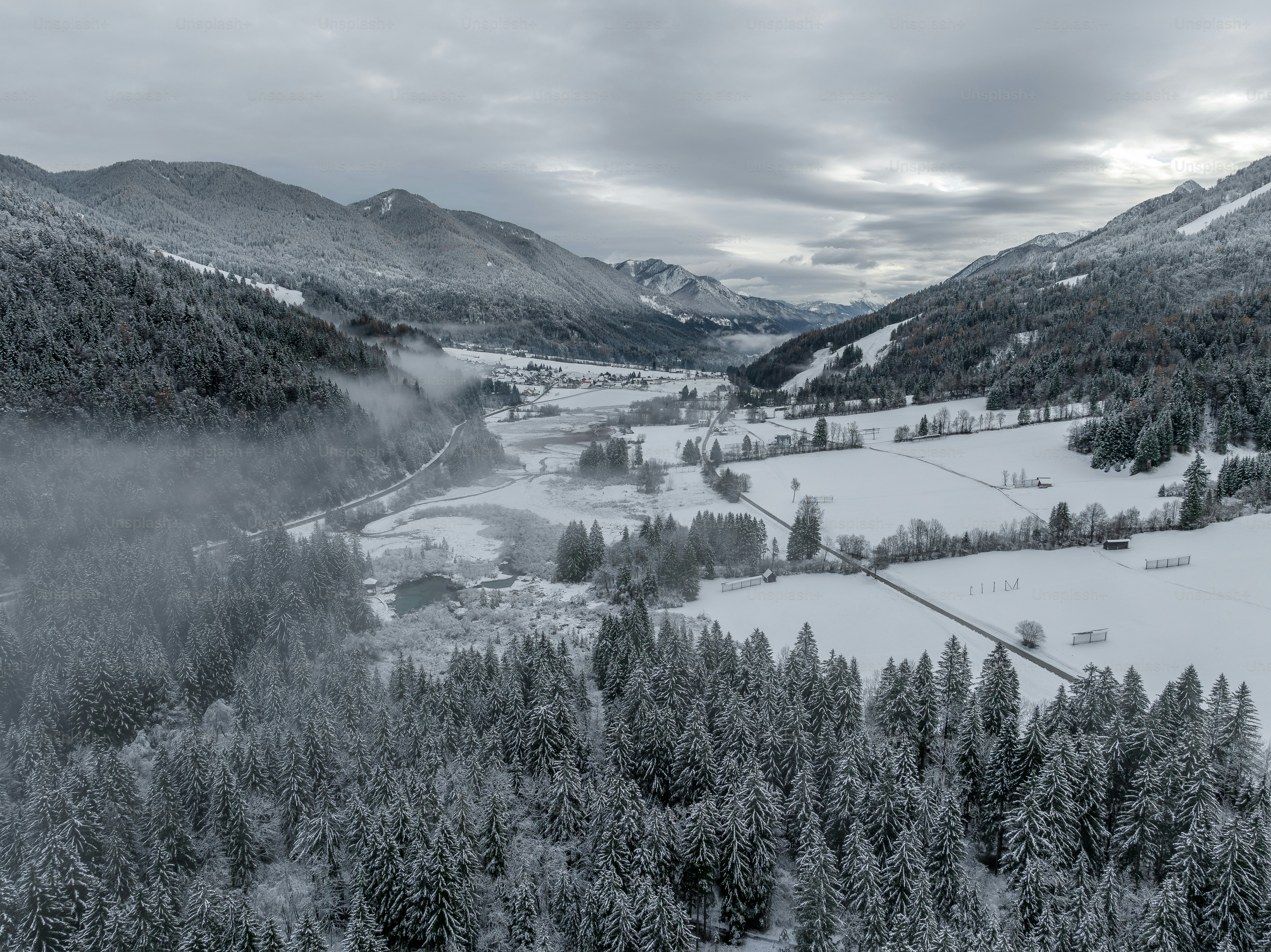 A snow covered valley surrounded by mountains and trees photo – Winter ...