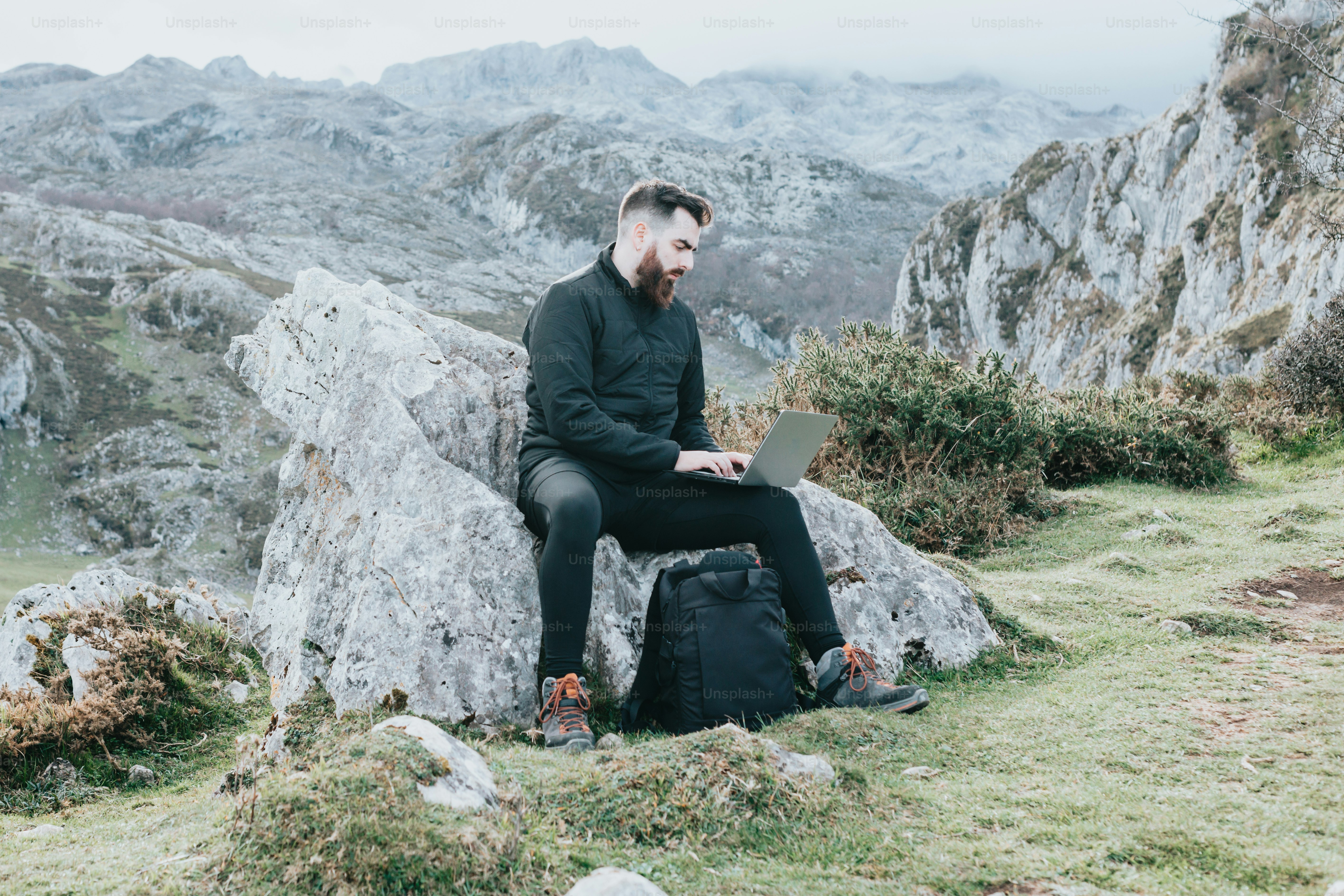 Foto Un hombre sentado en una roca usando una computadora portátil ...