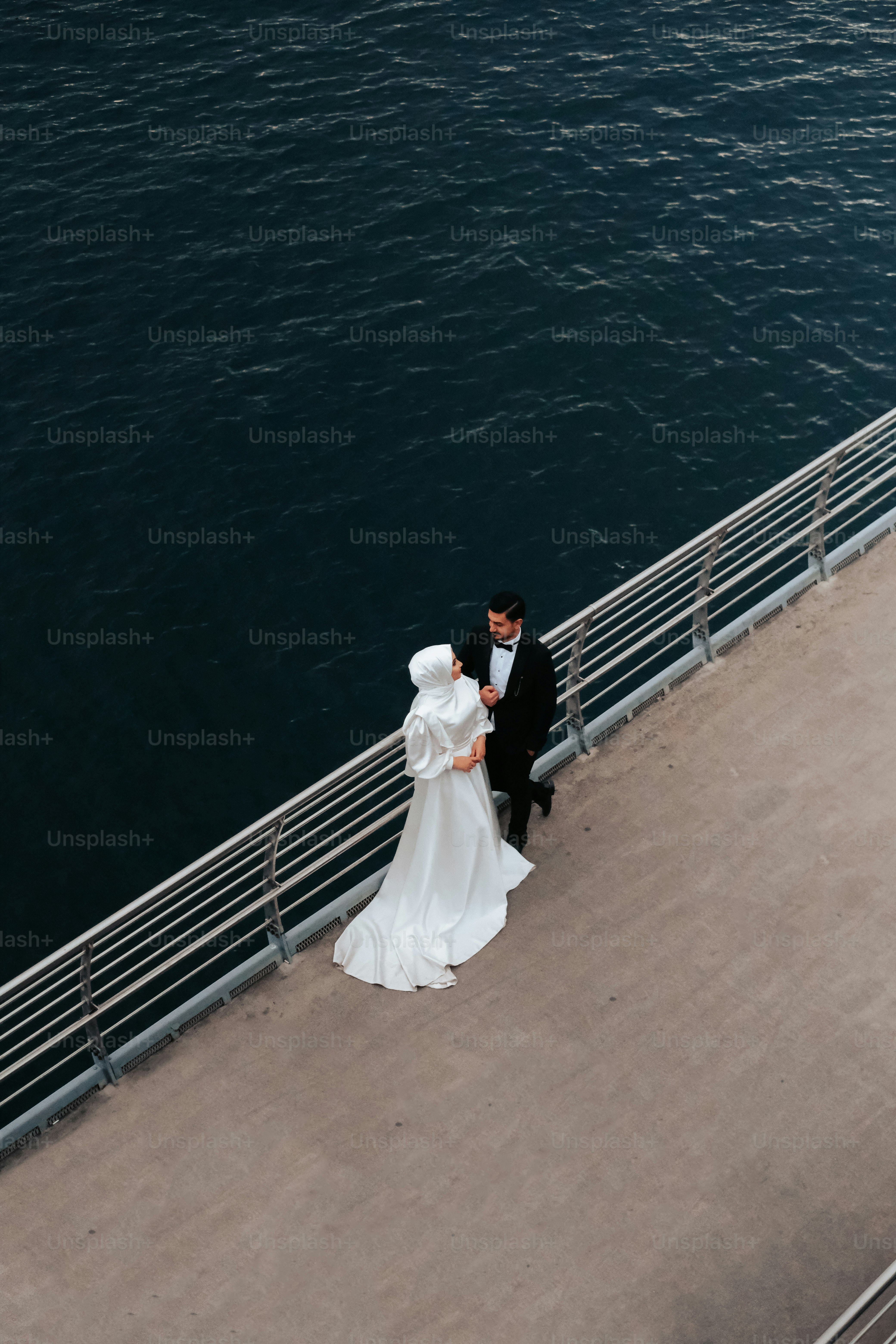 A bride and groom standing on a pier next to a body of water photo ...