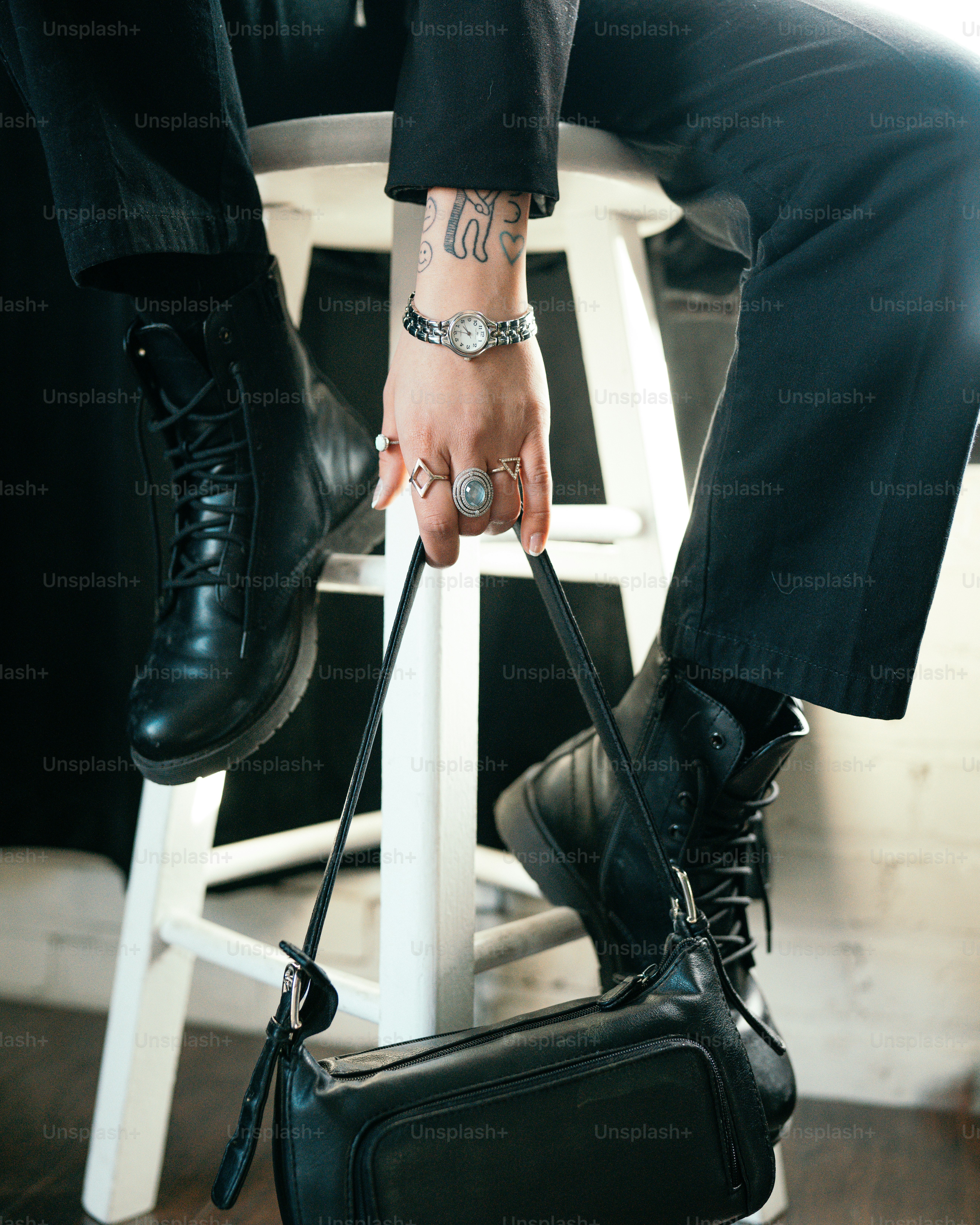 A person sitting on a stool holding a black bag photo – Handbag Image ...