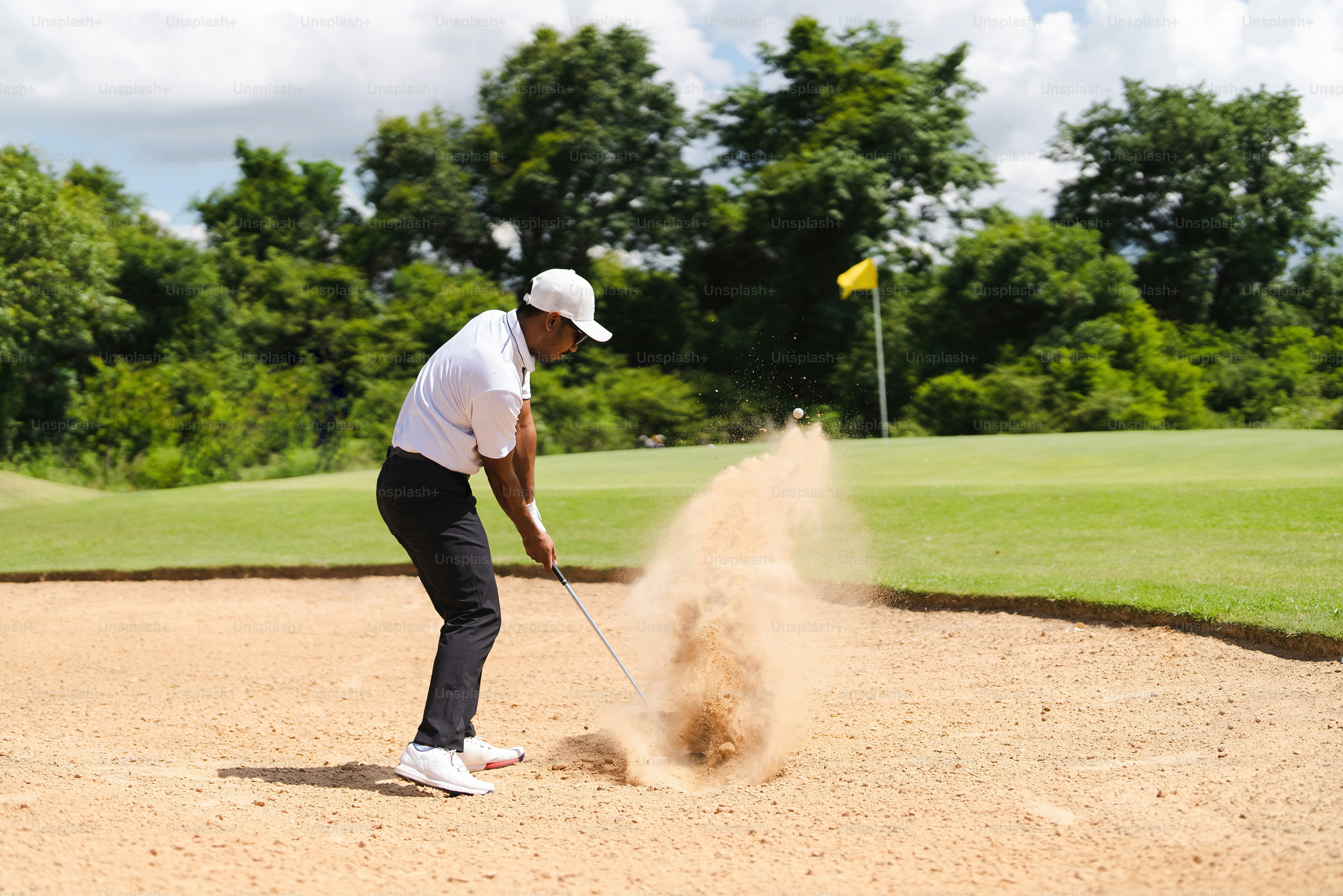 Asian man golfing on the course. He hits a golf ball on a sand field ...