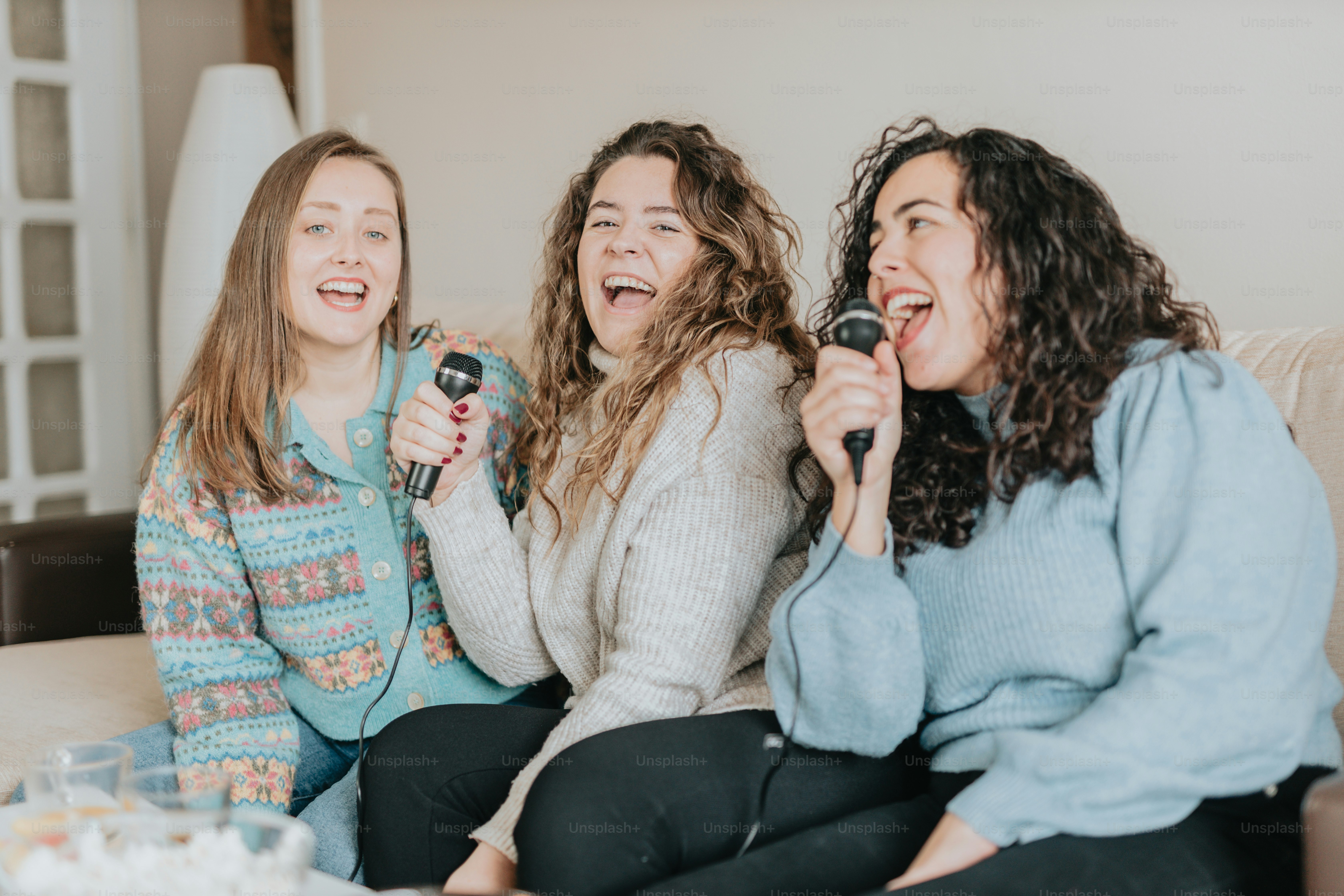 A group of women singing into microphones while sitting on a couch ...