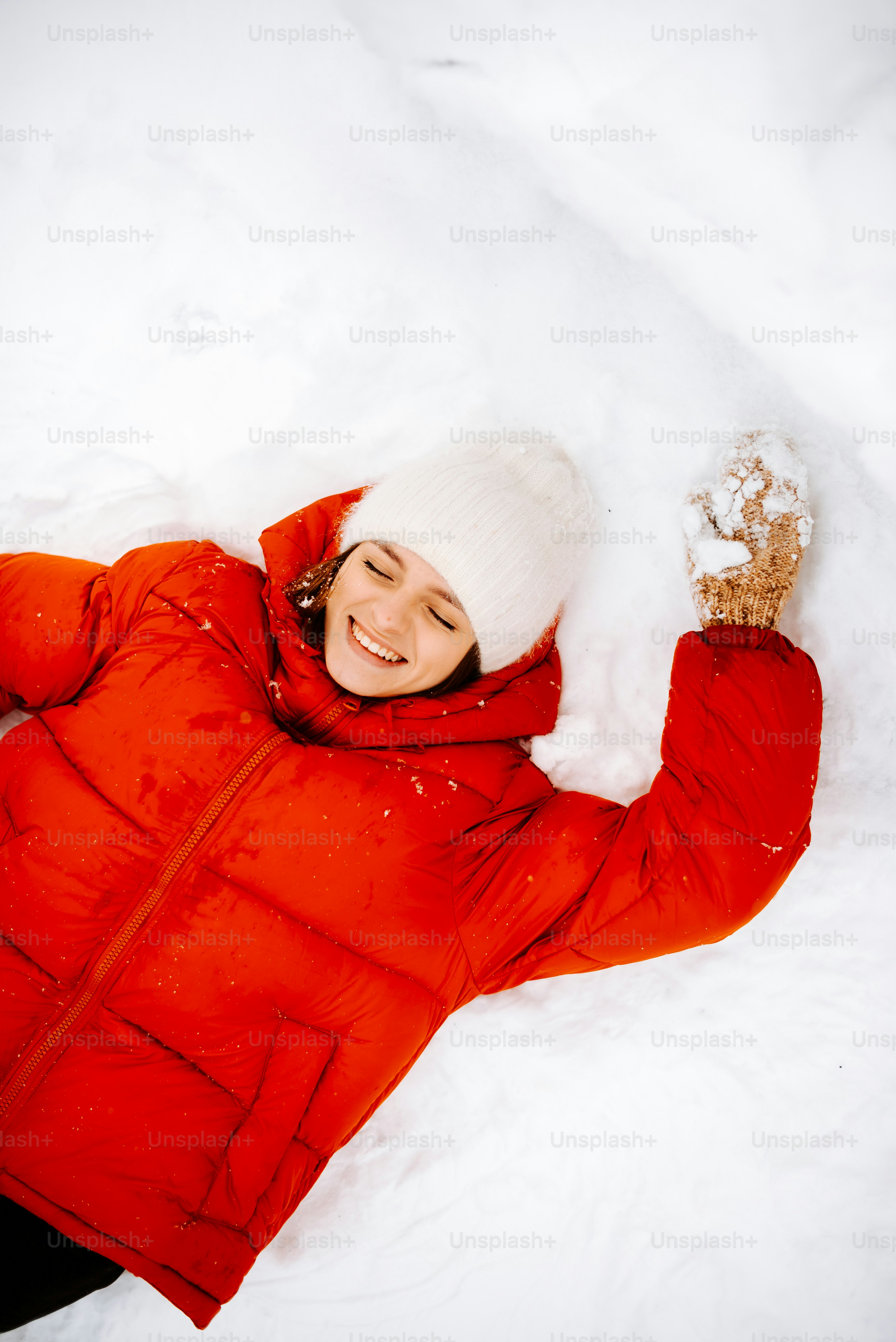 A woman in a red jacket laying in the snow photo – Down jacket Image on ...