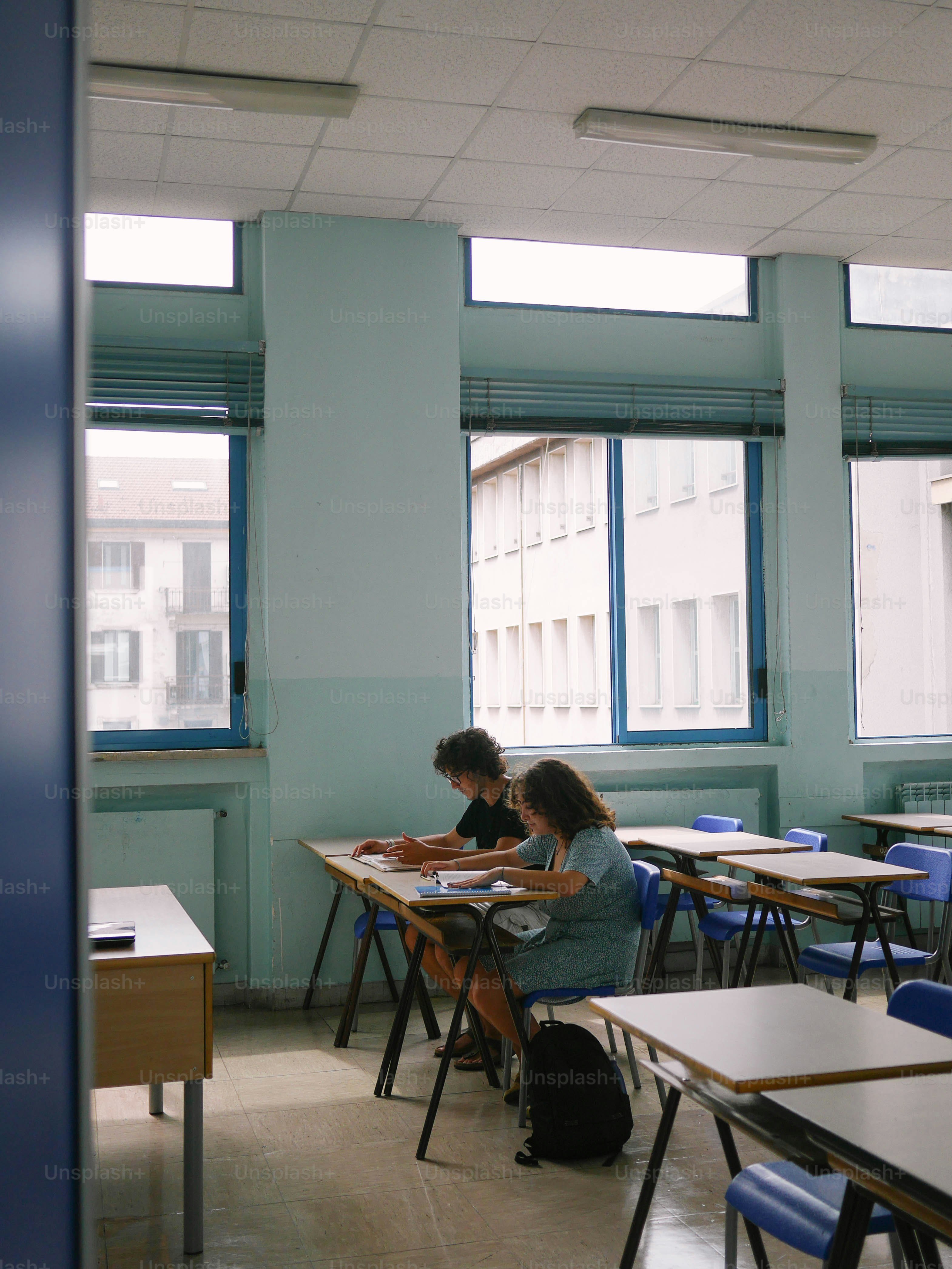 A couple of people sitting at desks in a room photo – Study Image on ...