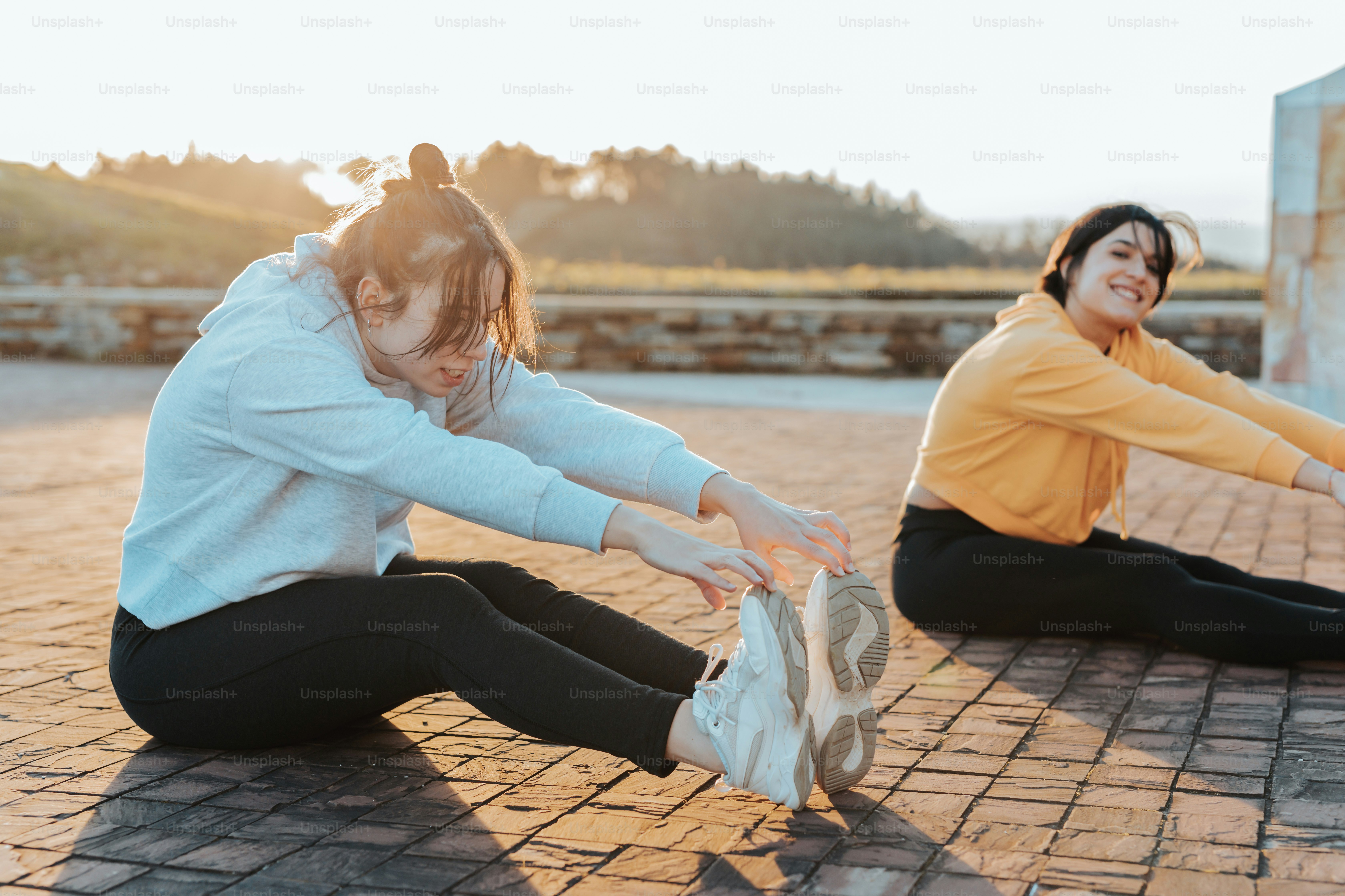 Two women sitting on the ground stretching their legs photo – Fitness ...