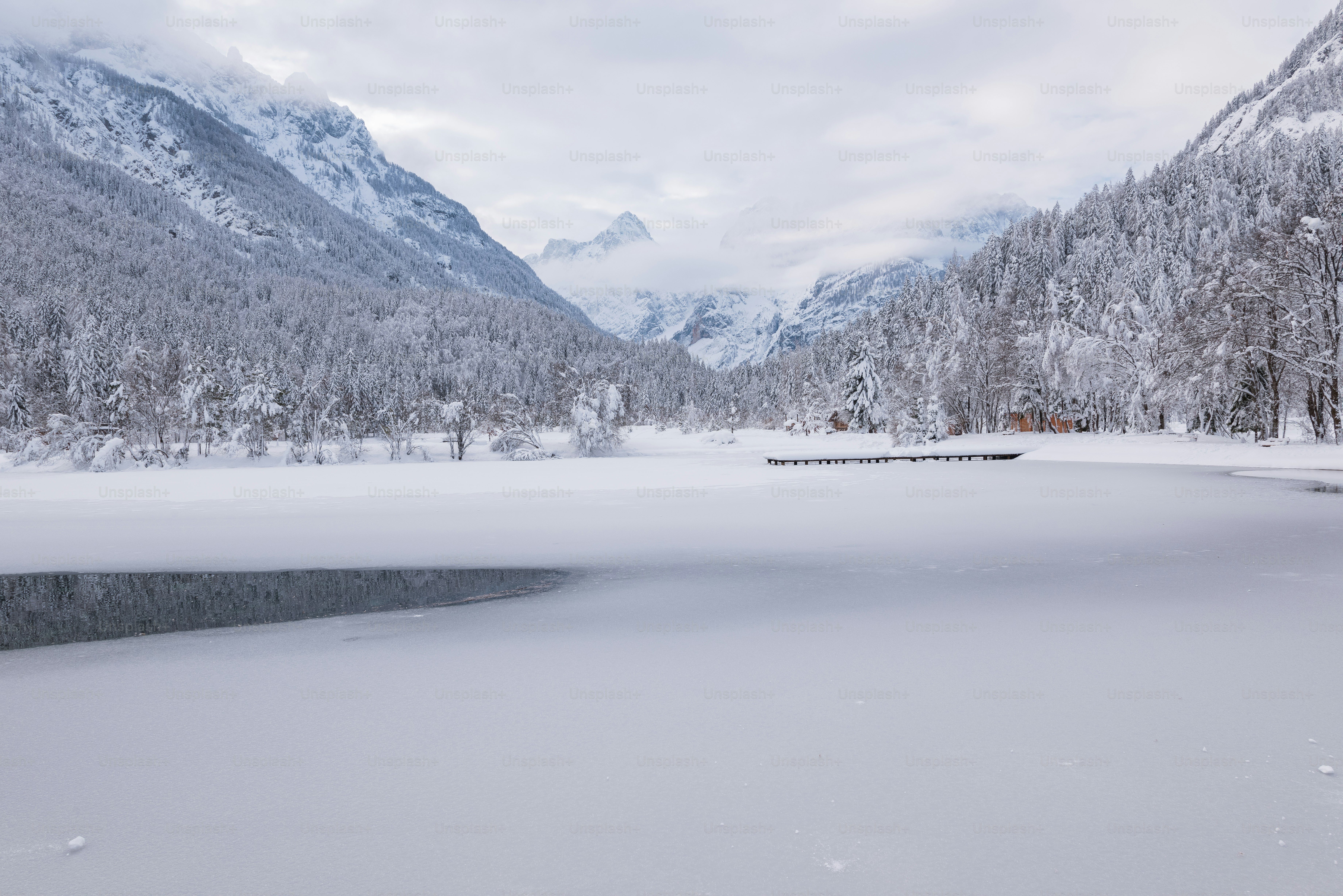 Un lago rodeado de montañas cubiertas de nieve y árboles foto – Imagen ...