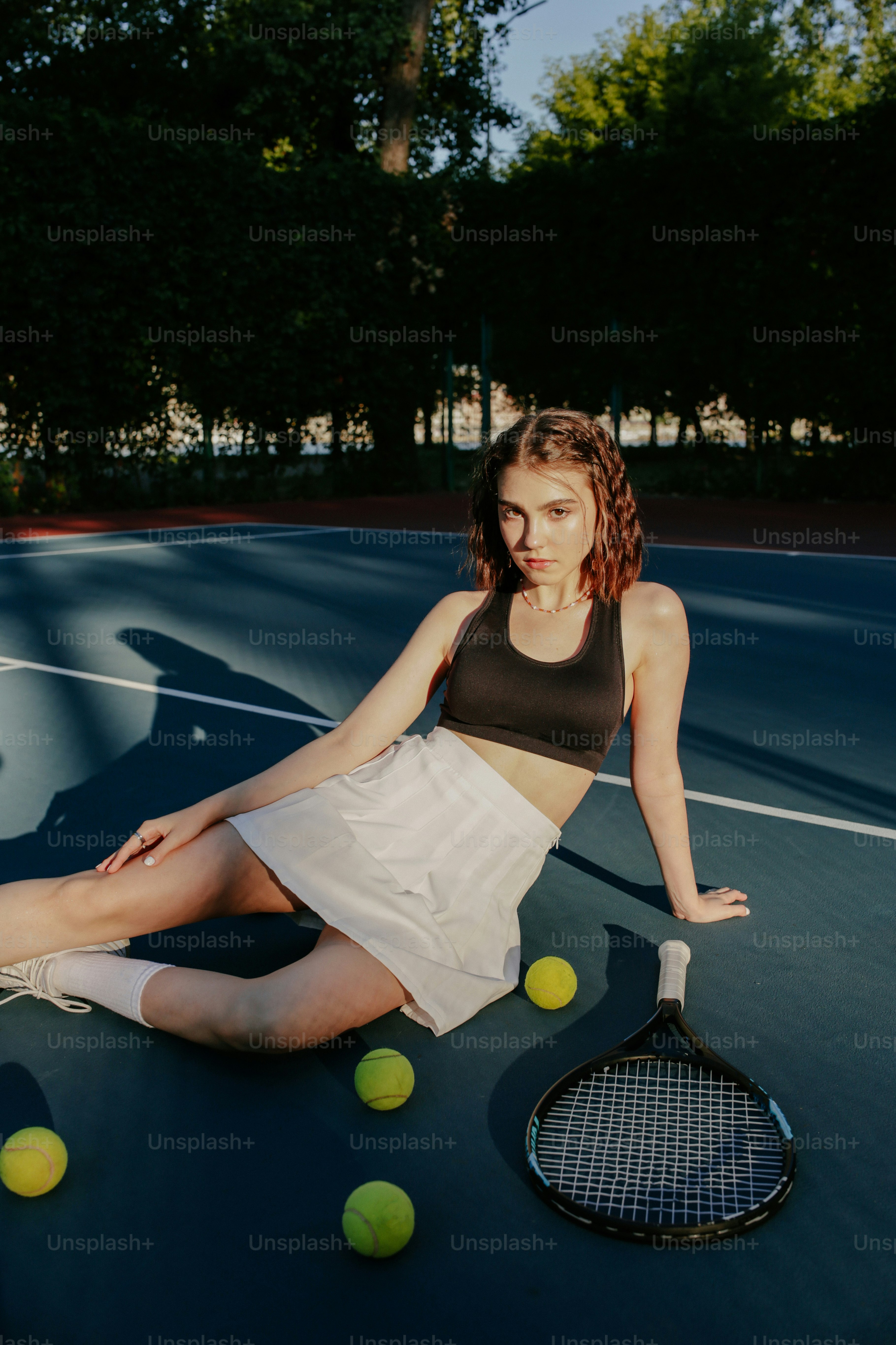 A woman sitting on a tennis court holding a tennis racket photo ...
