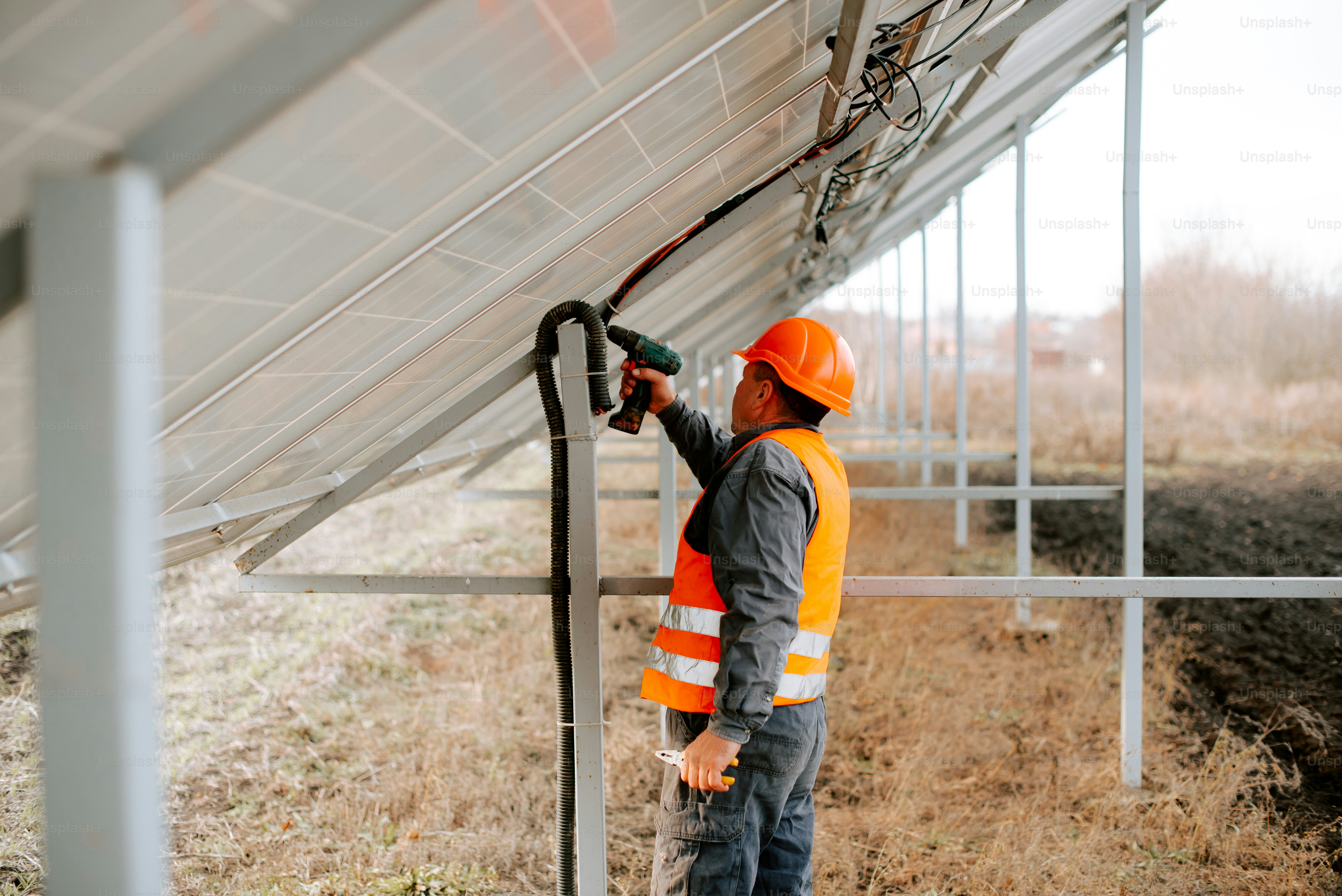 A man in an orange safety vest is fixing a solar panel photo ...