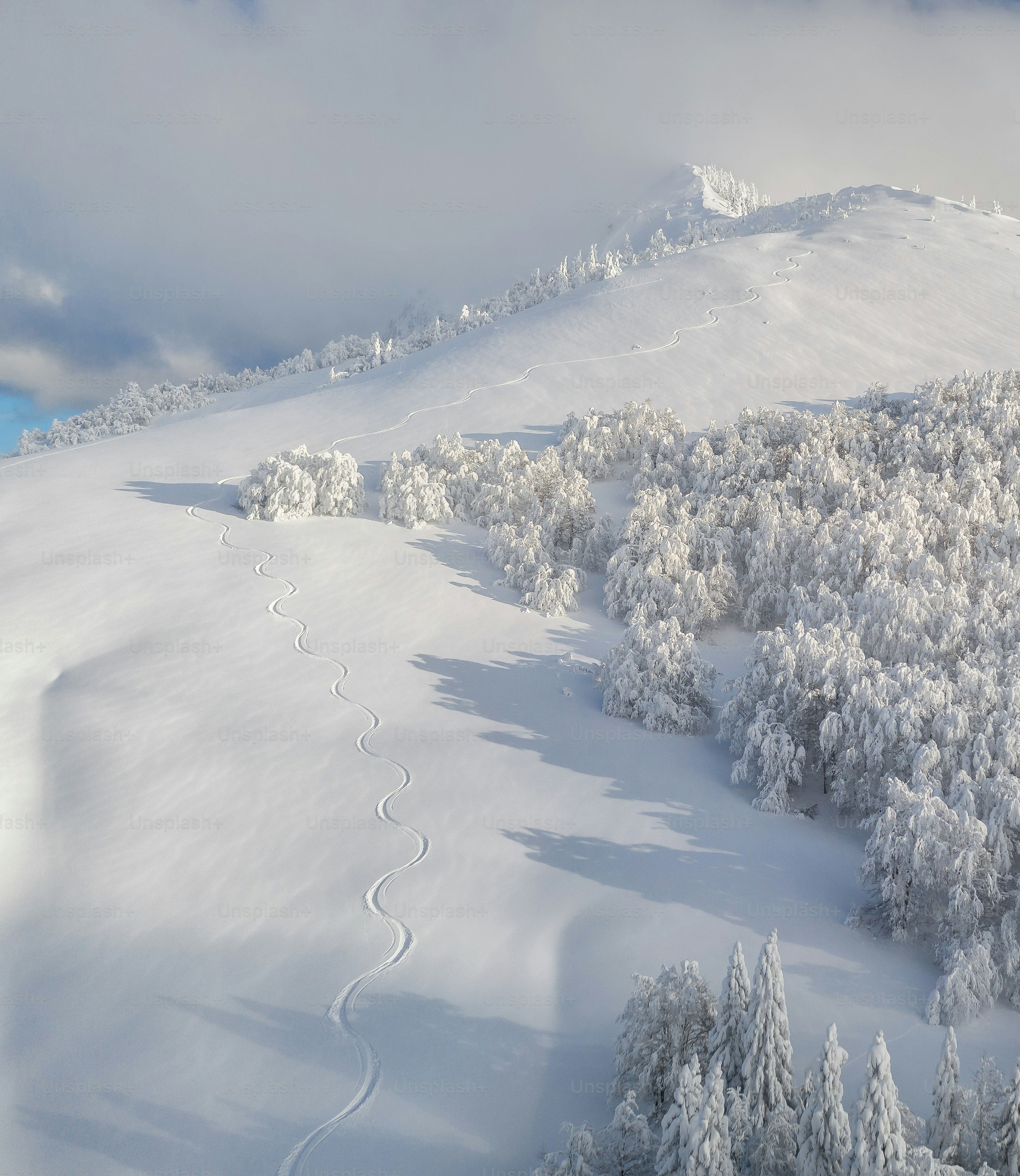 A snow covered mountain with tracks in the snow photo – Snow mountain ...