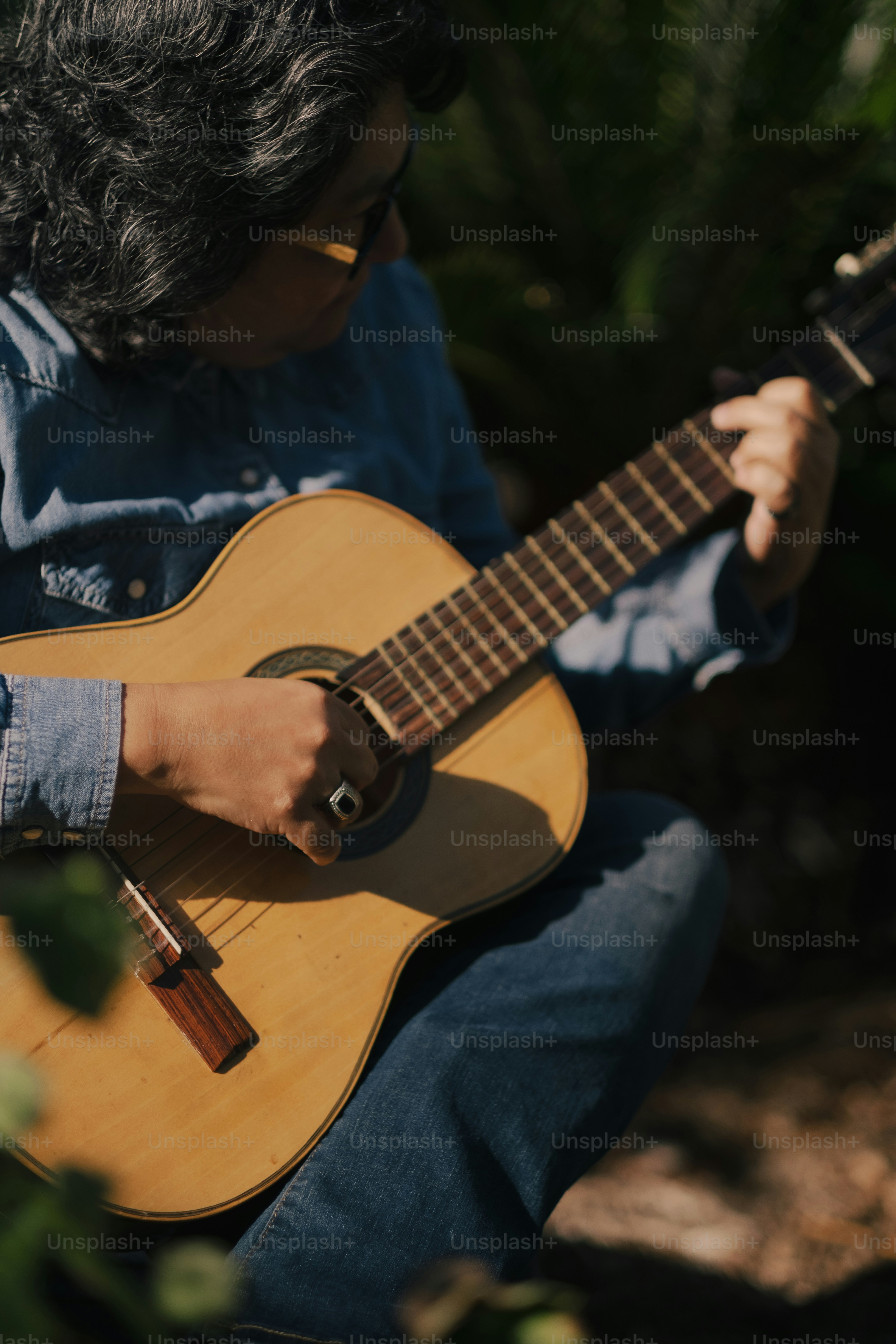 A man sitting down playing a guitar outside photo – Guitarist Image on ...