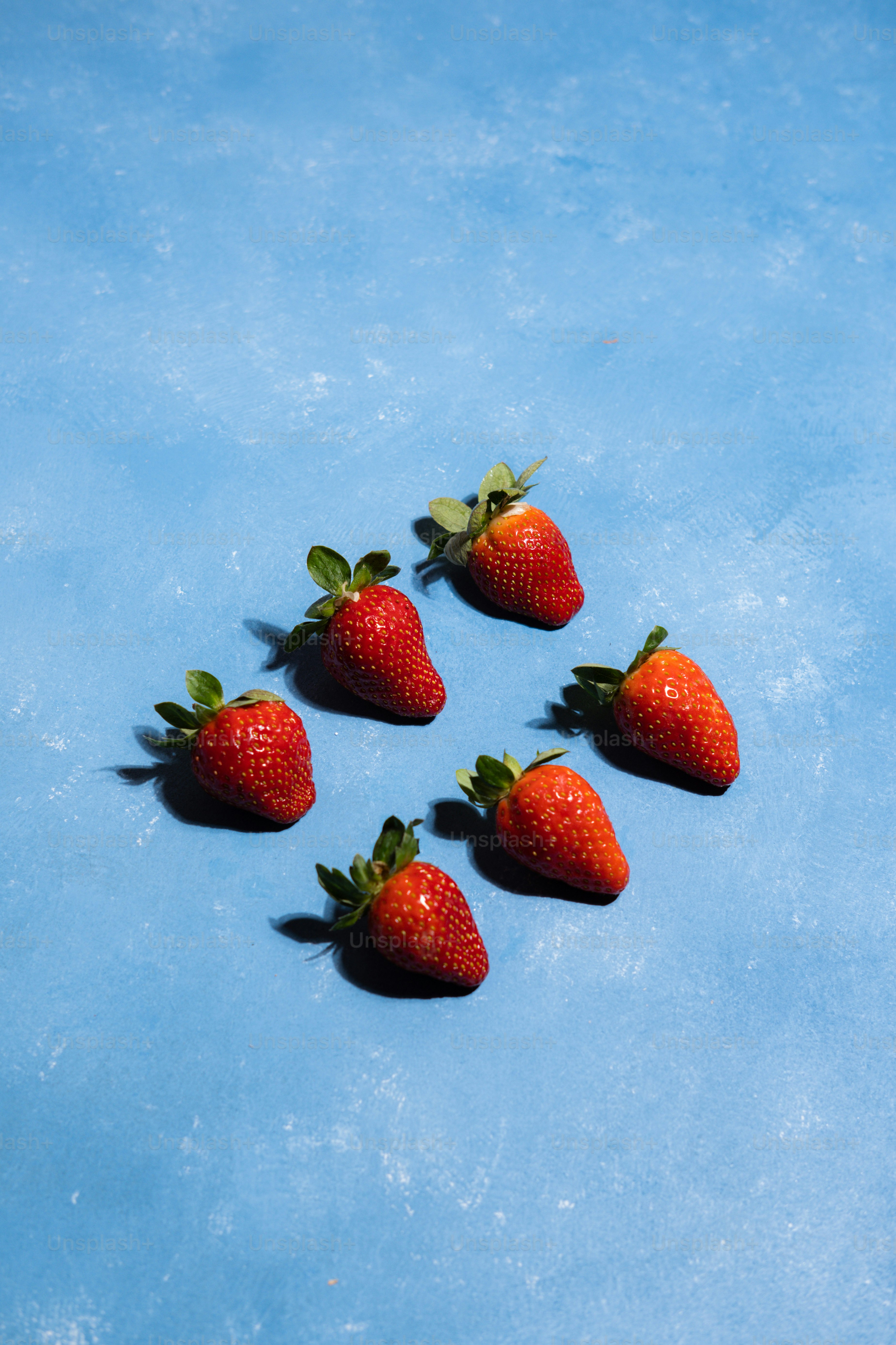 A group of five strawberries on a blue surface photo – Fresas Image on ...