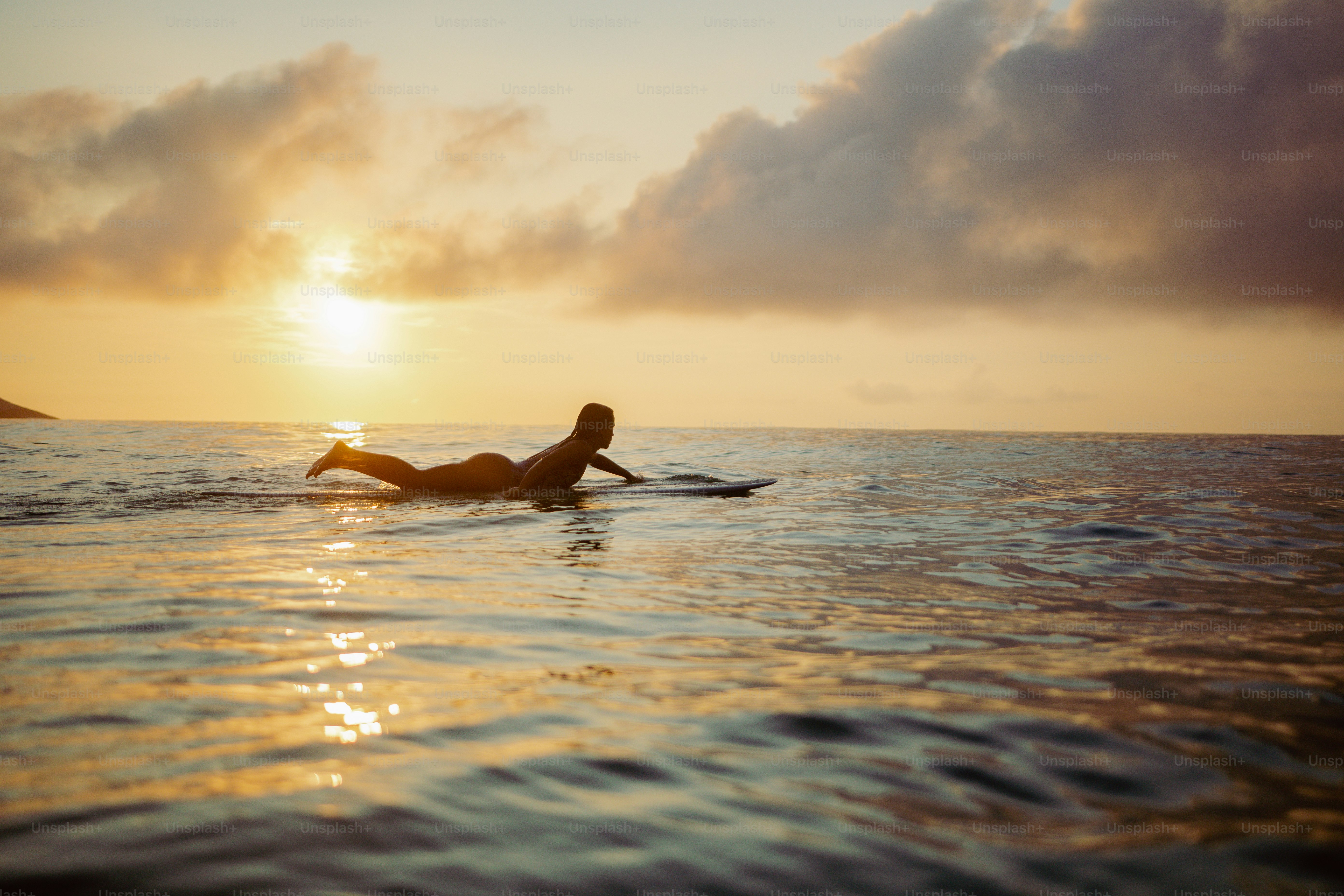 A woman laying on a surfboard in the ocean at sunset photo – Nature ...