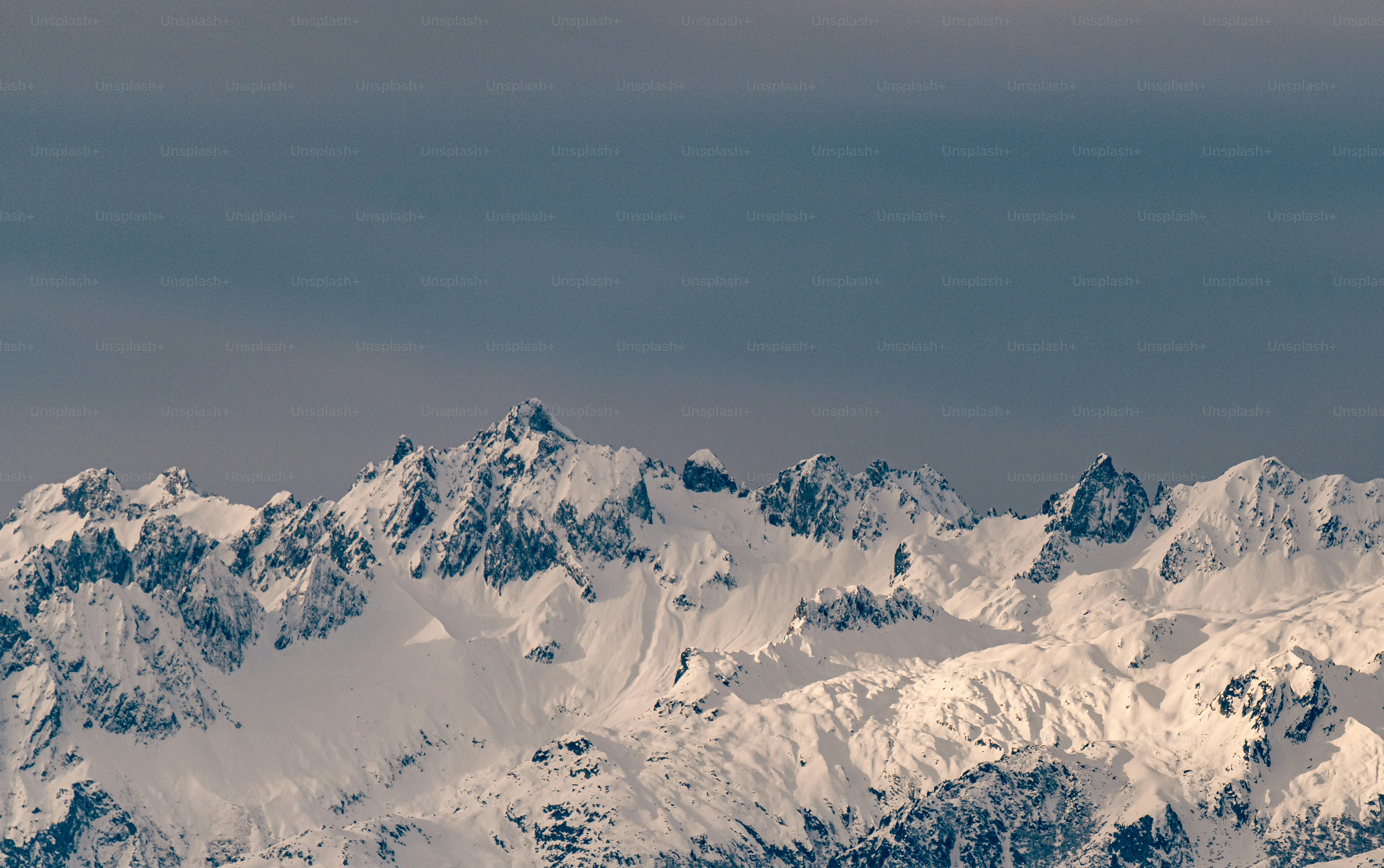 A plane flying over a snow covered mountain range photo – Wallpaper ...