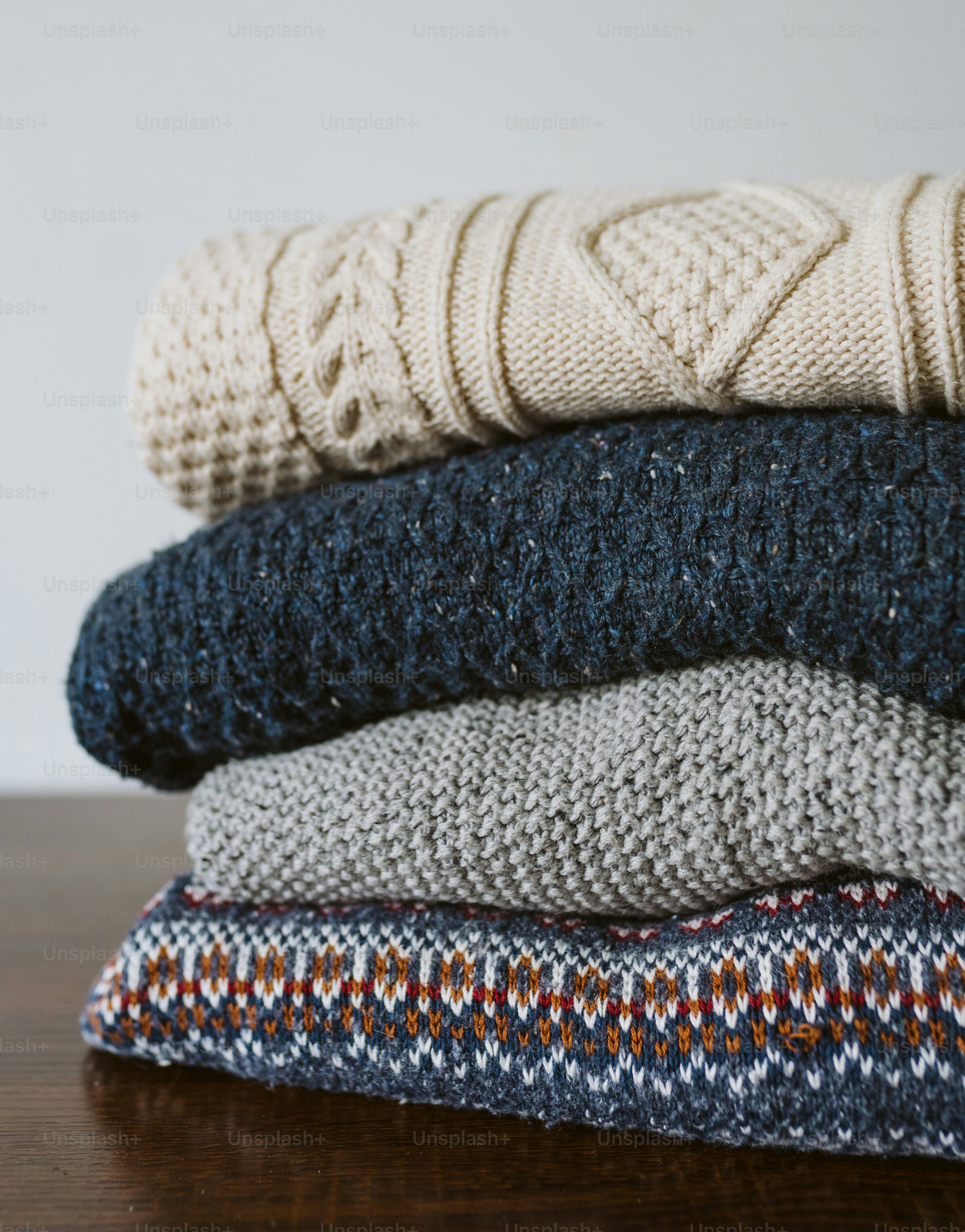 A stack of folded sweaters sitting on top of a wooden table photo ...