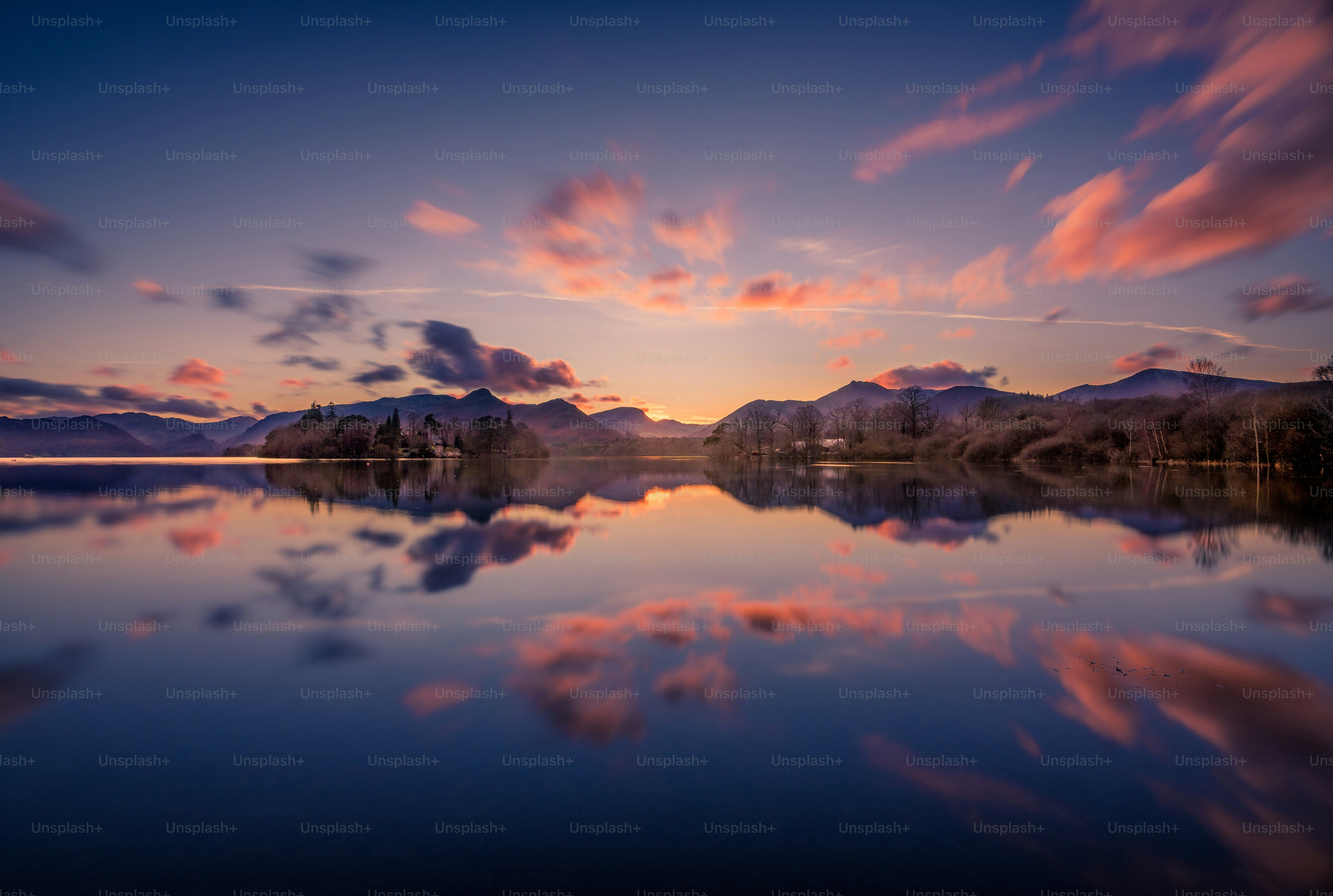 The sun is setting over a lake with mountains in the background photo ...