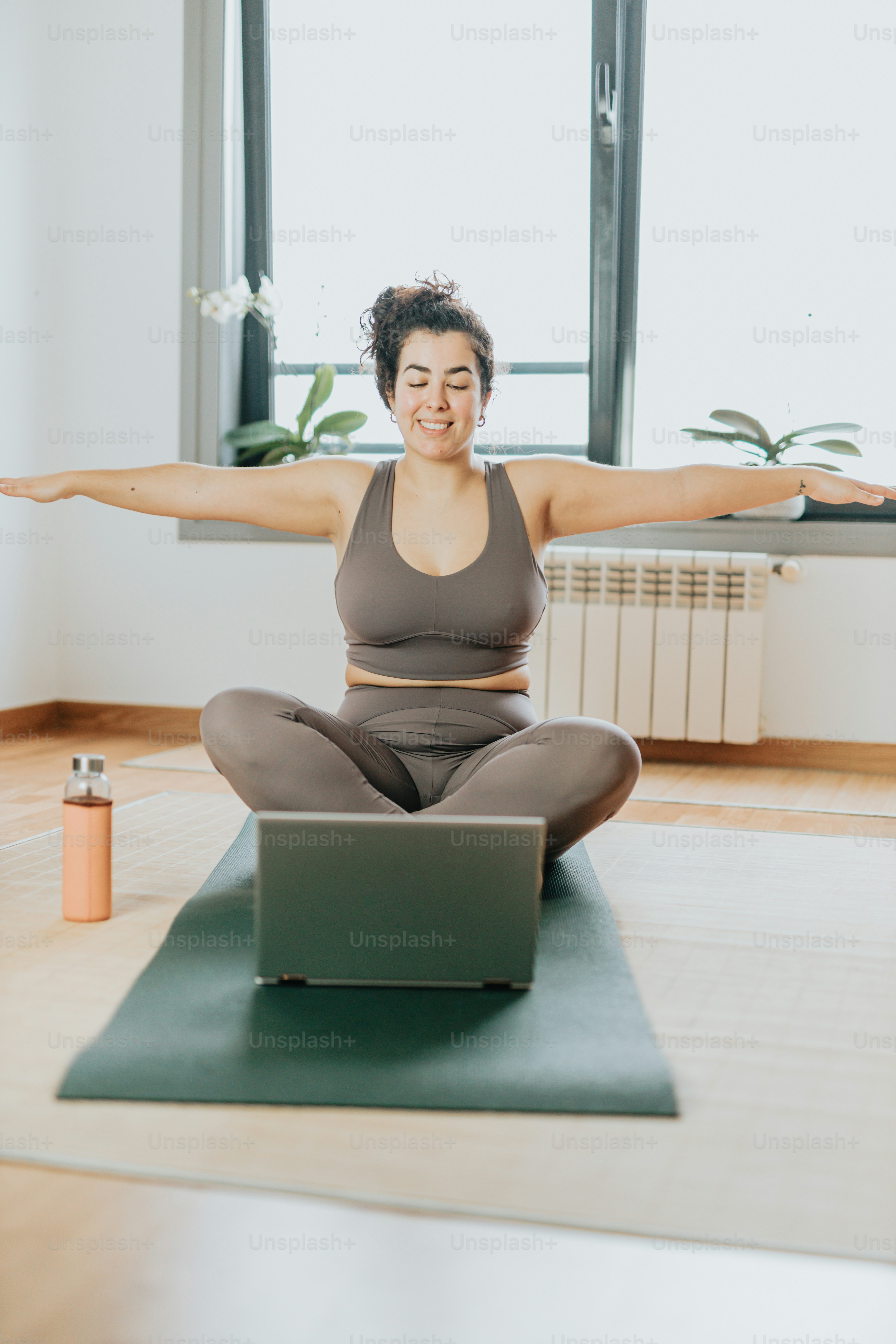 Una mujer sentada en una esterilla de yoga frente a una computadora ...