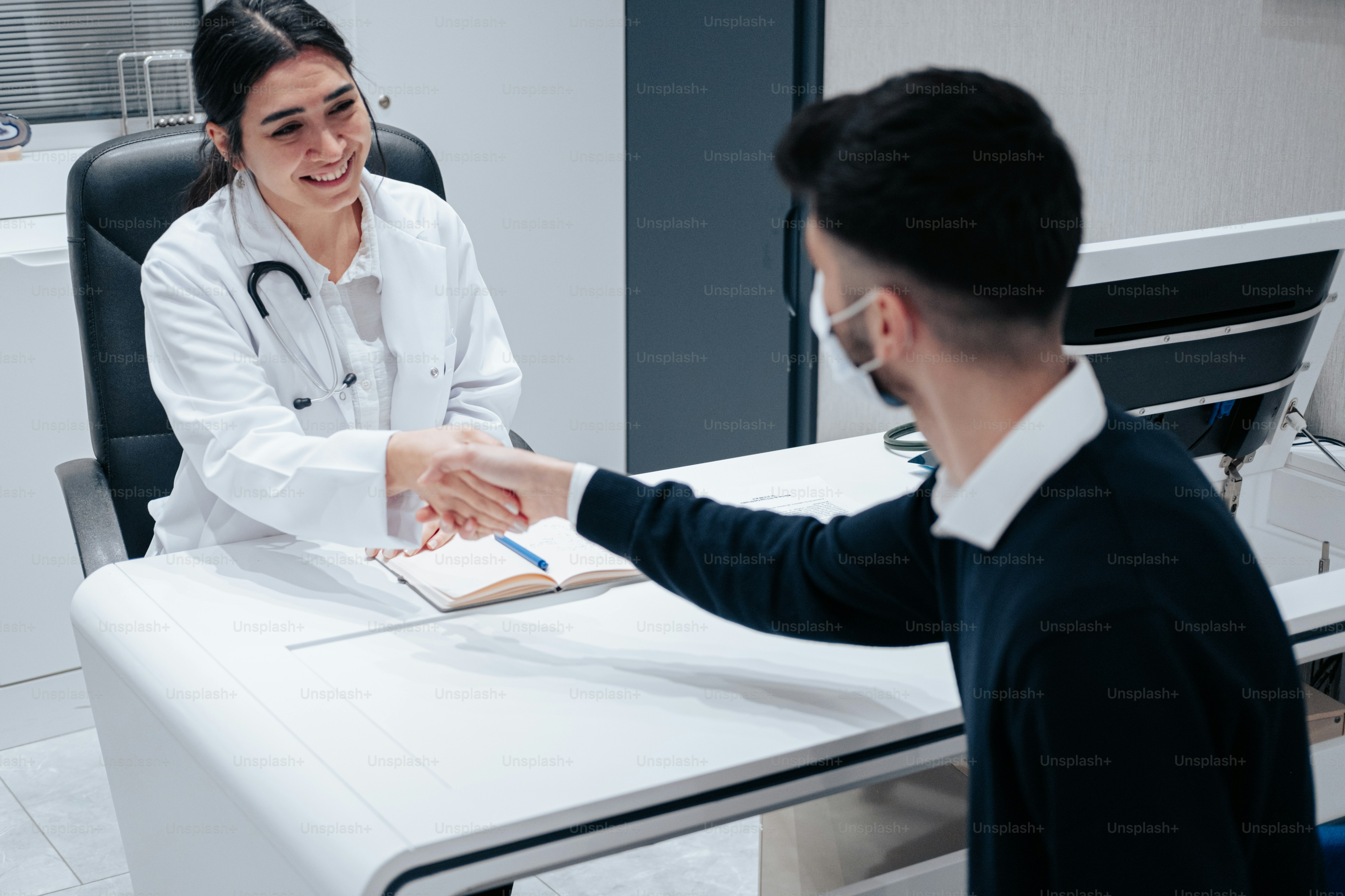 A doctor shaking hands with a patient at a desk photo – Patient Image ...