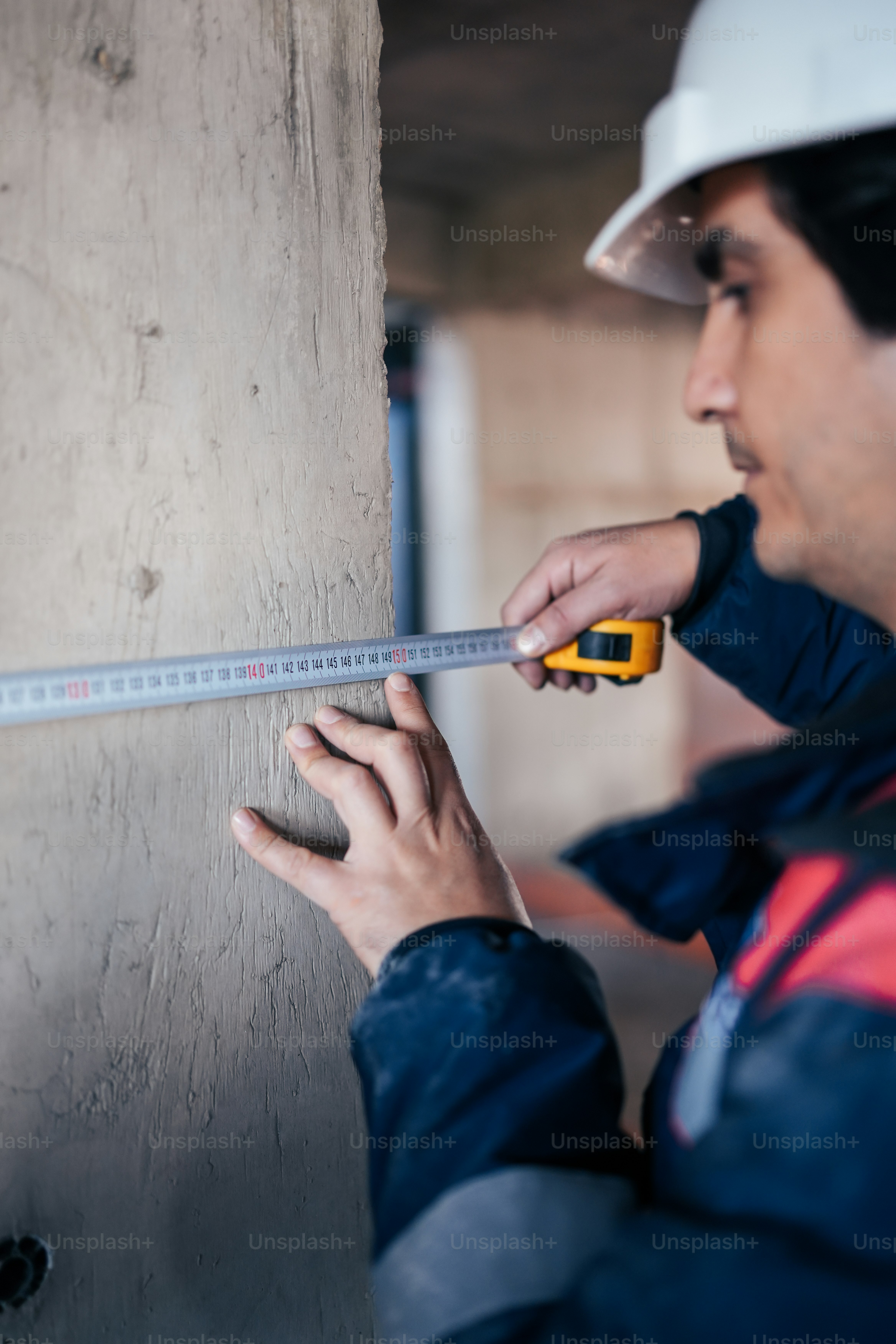 A man in a hard hat measuring a wall with a tape measure photo – Meter ...