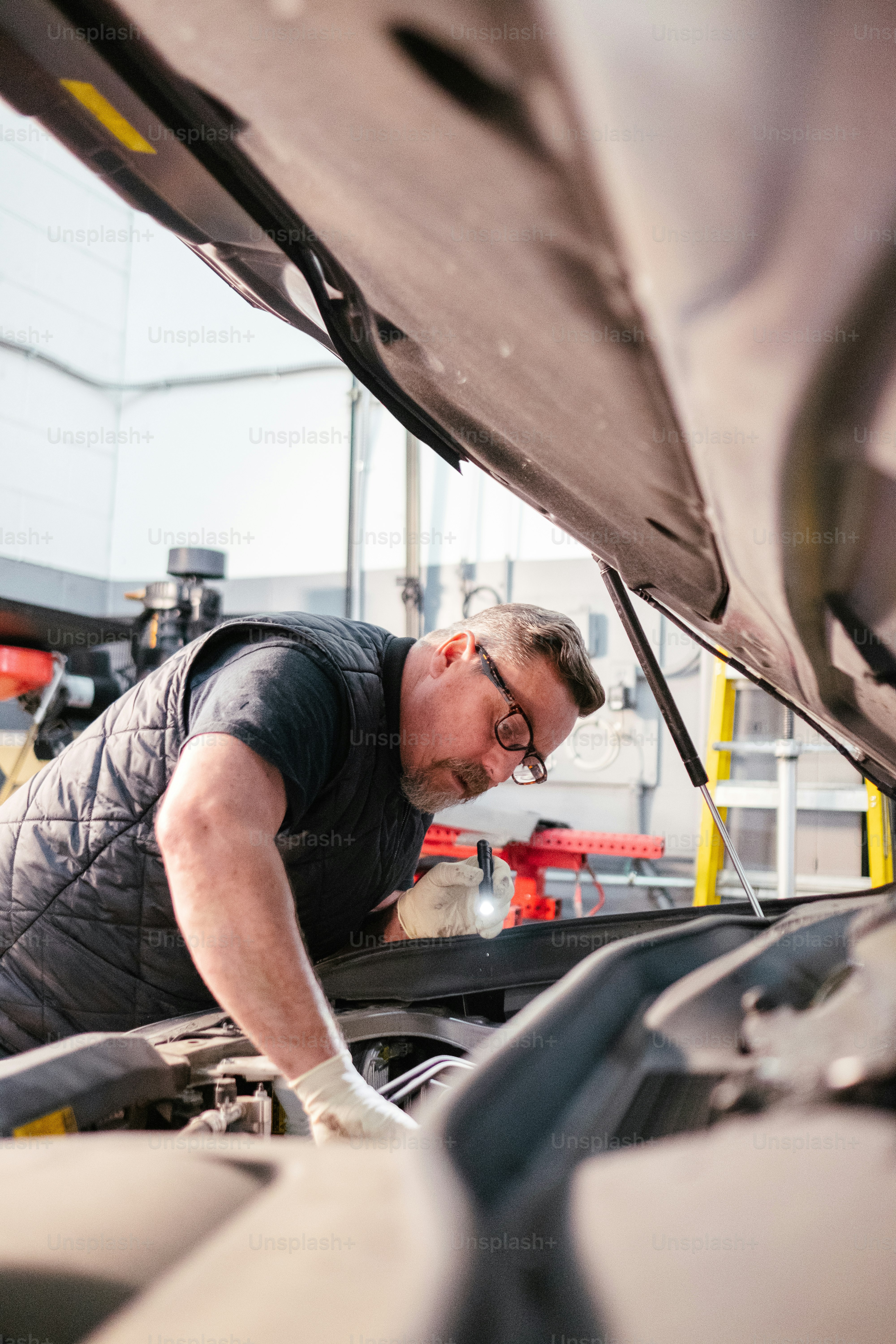 A man working on a car engine in a garage photo – Car mechanic Image on ...