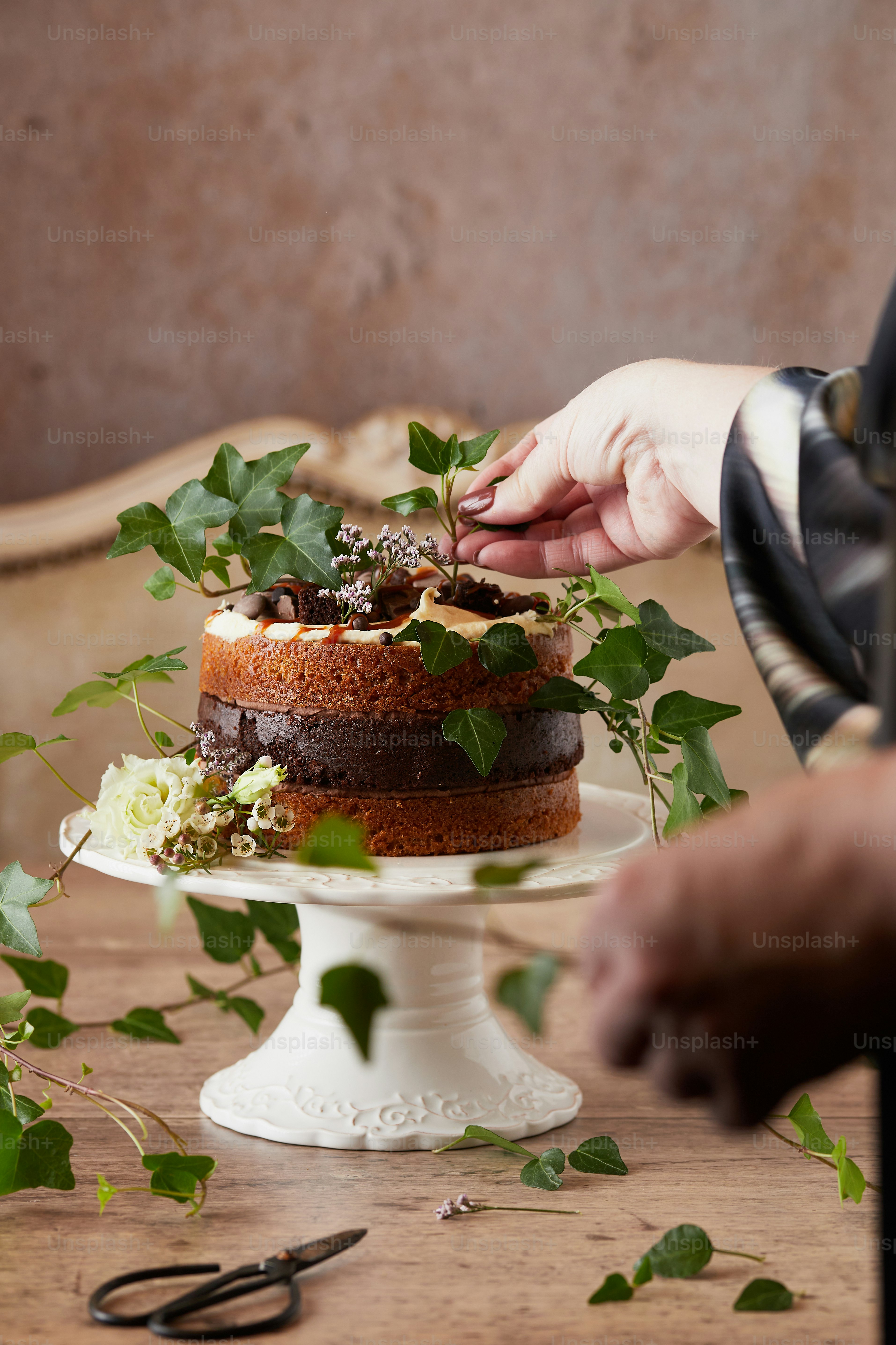 A person decorating a cake with greenery on a table photo – Wedding ...
