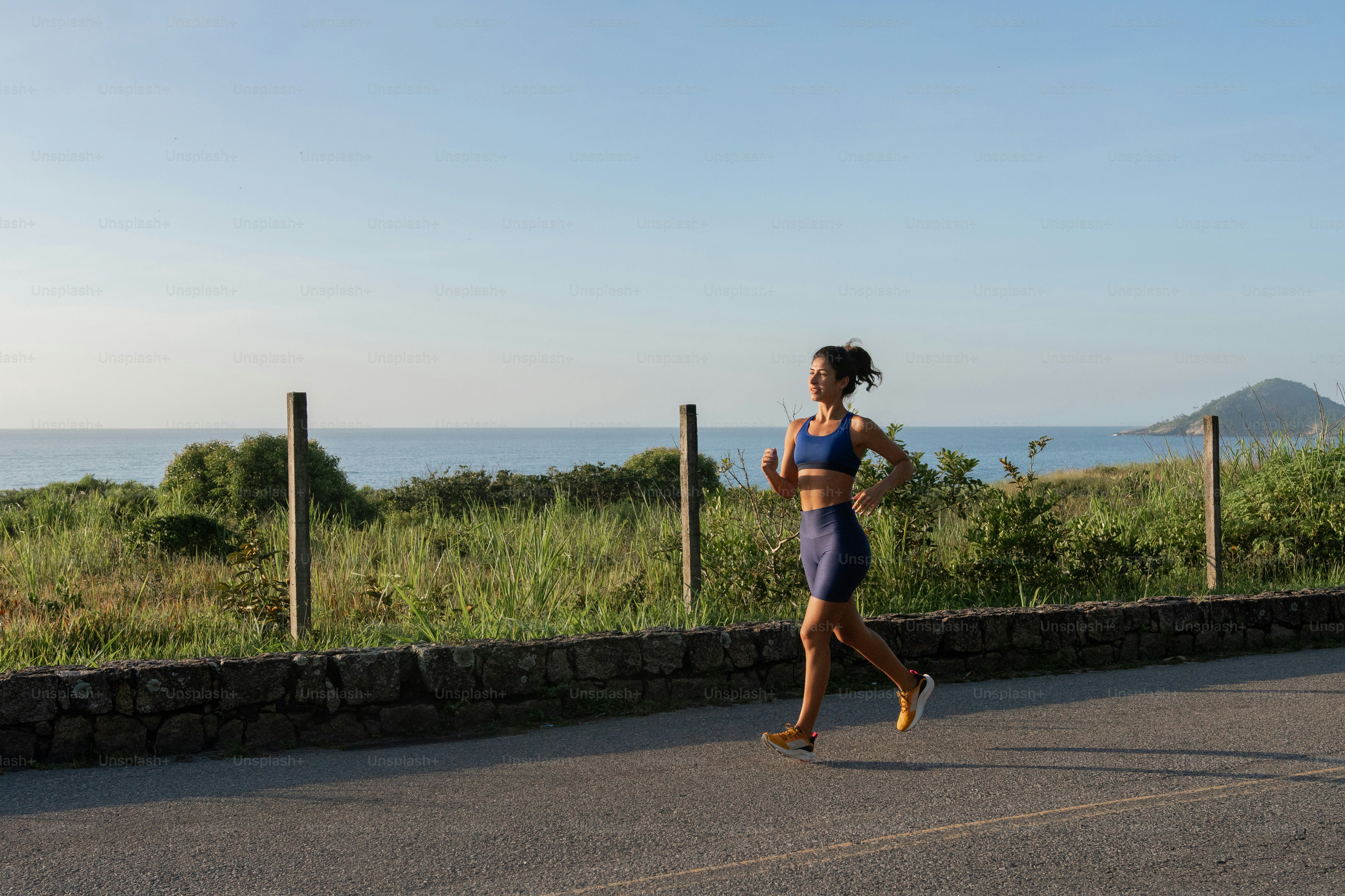 A woman running down a road next to the ocean photo – Running girl ...