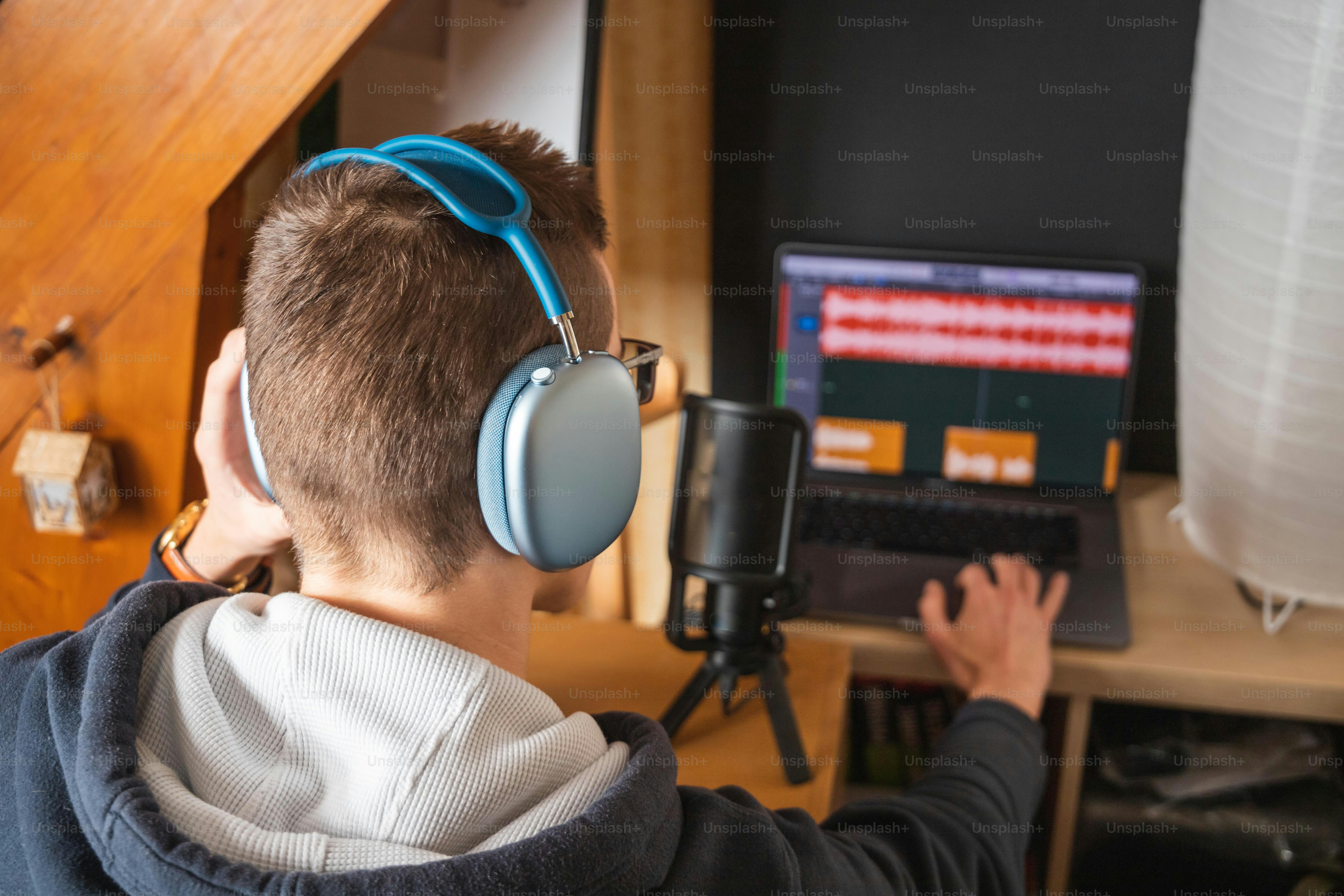 A young man wearing headphones and looking at a computer screen photo ...