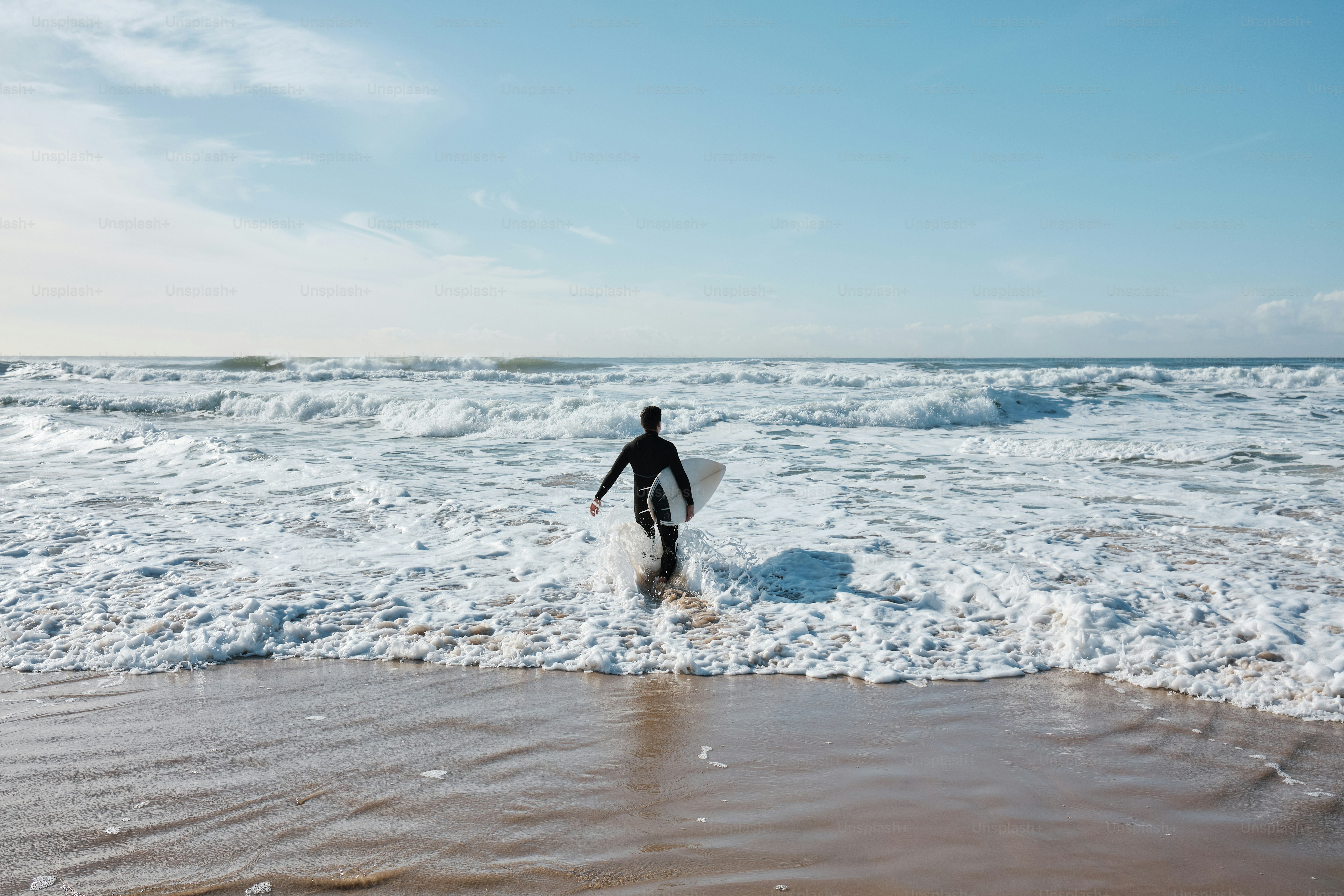 A person walking into the ocean with a surfboard photo – Surfing Image ...