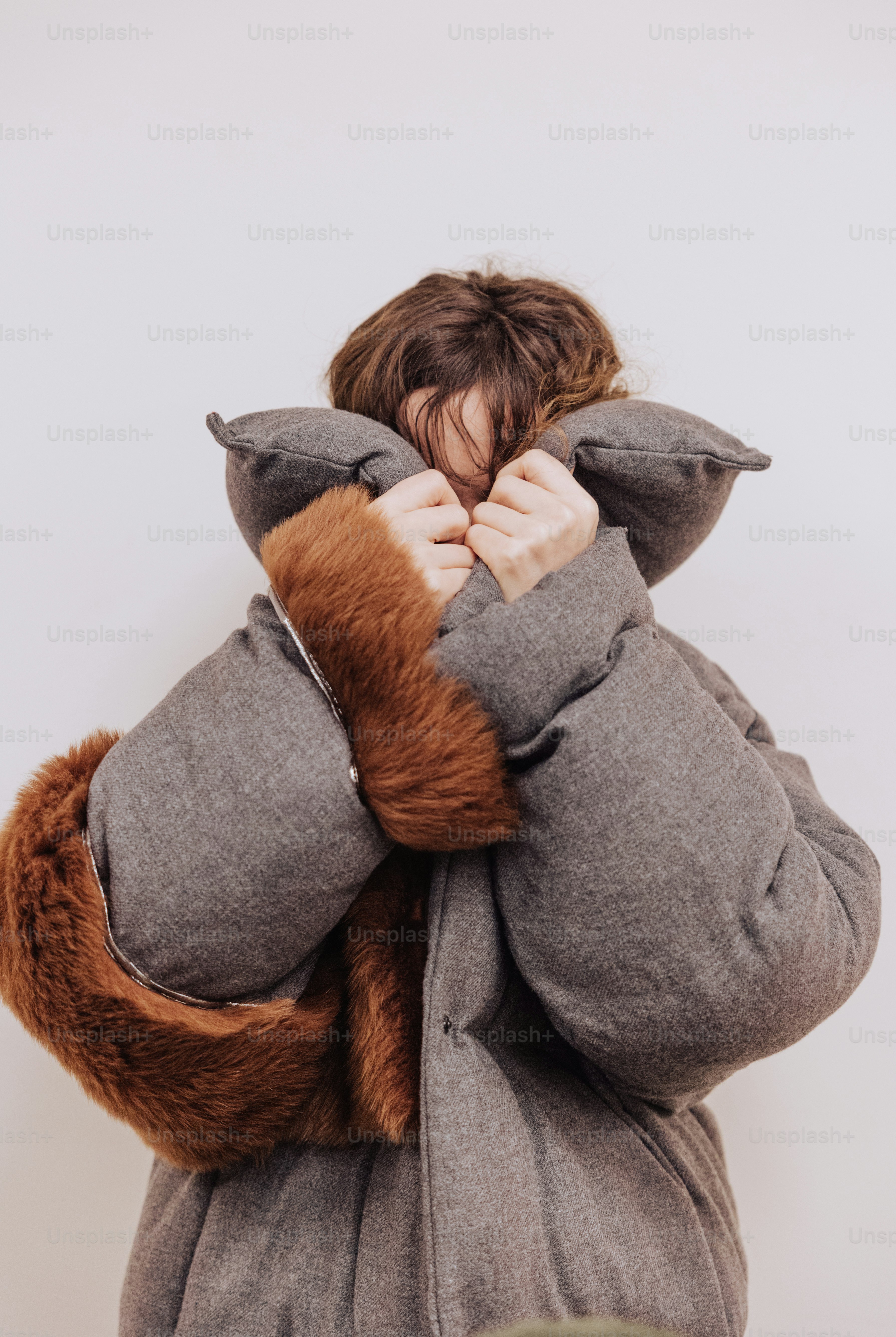 A woman is covering her face with her coat photo – Down jacket Image on ...