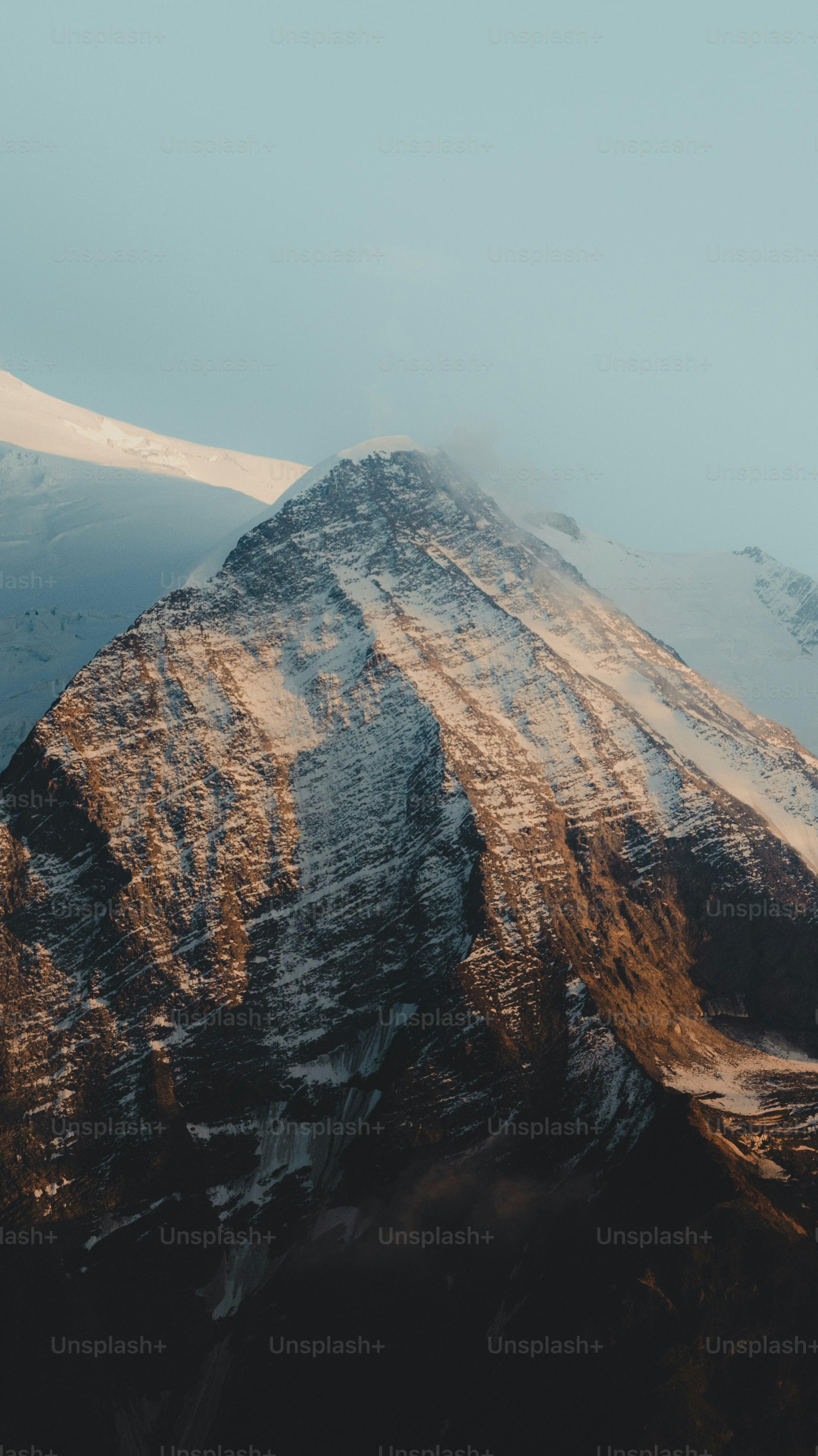 A very tall mountain covered in snow under a cloudy sky photo ...