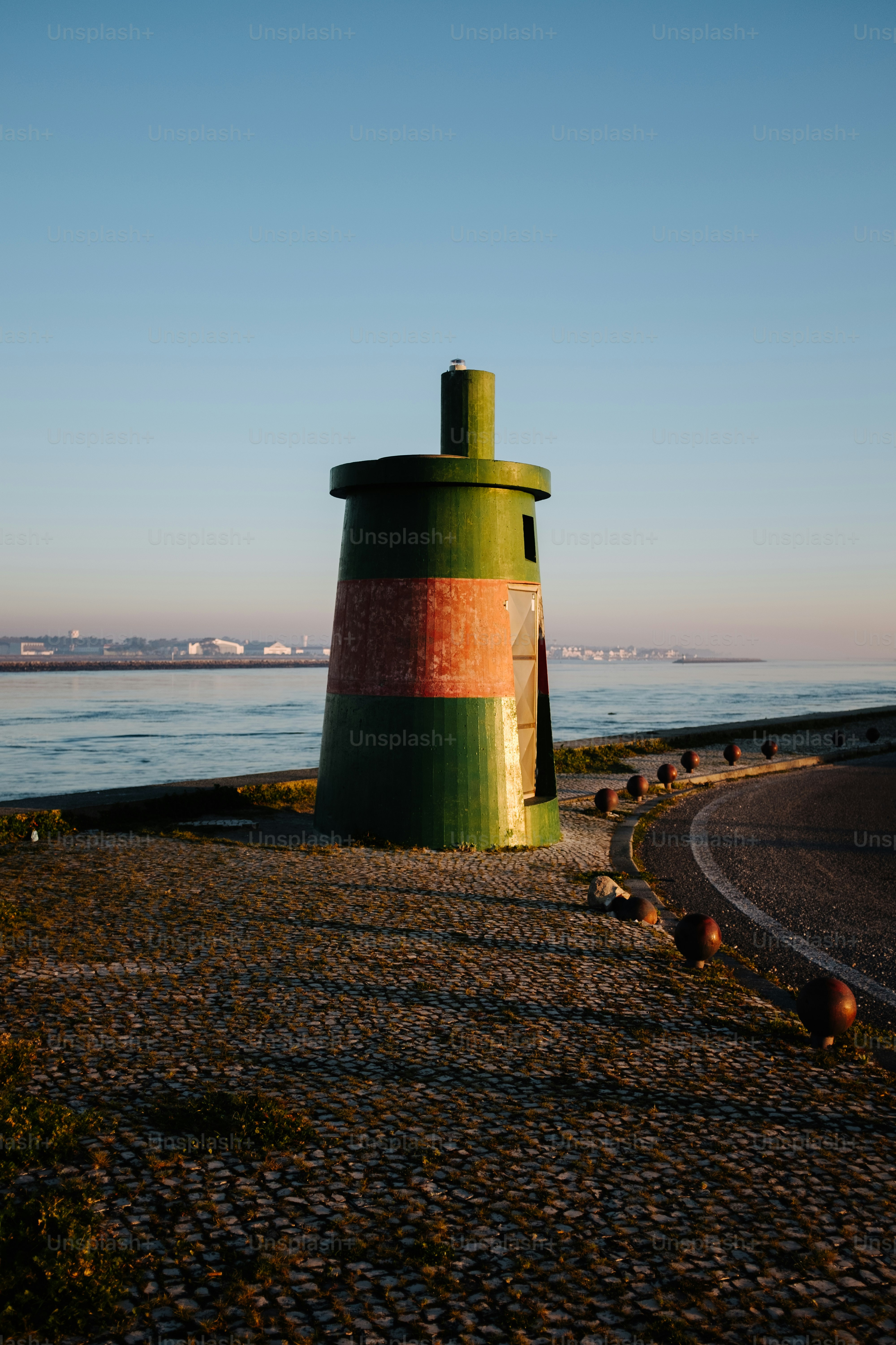 A green and red lighthouse sitting on the side of a road photo – Aveiro ...
