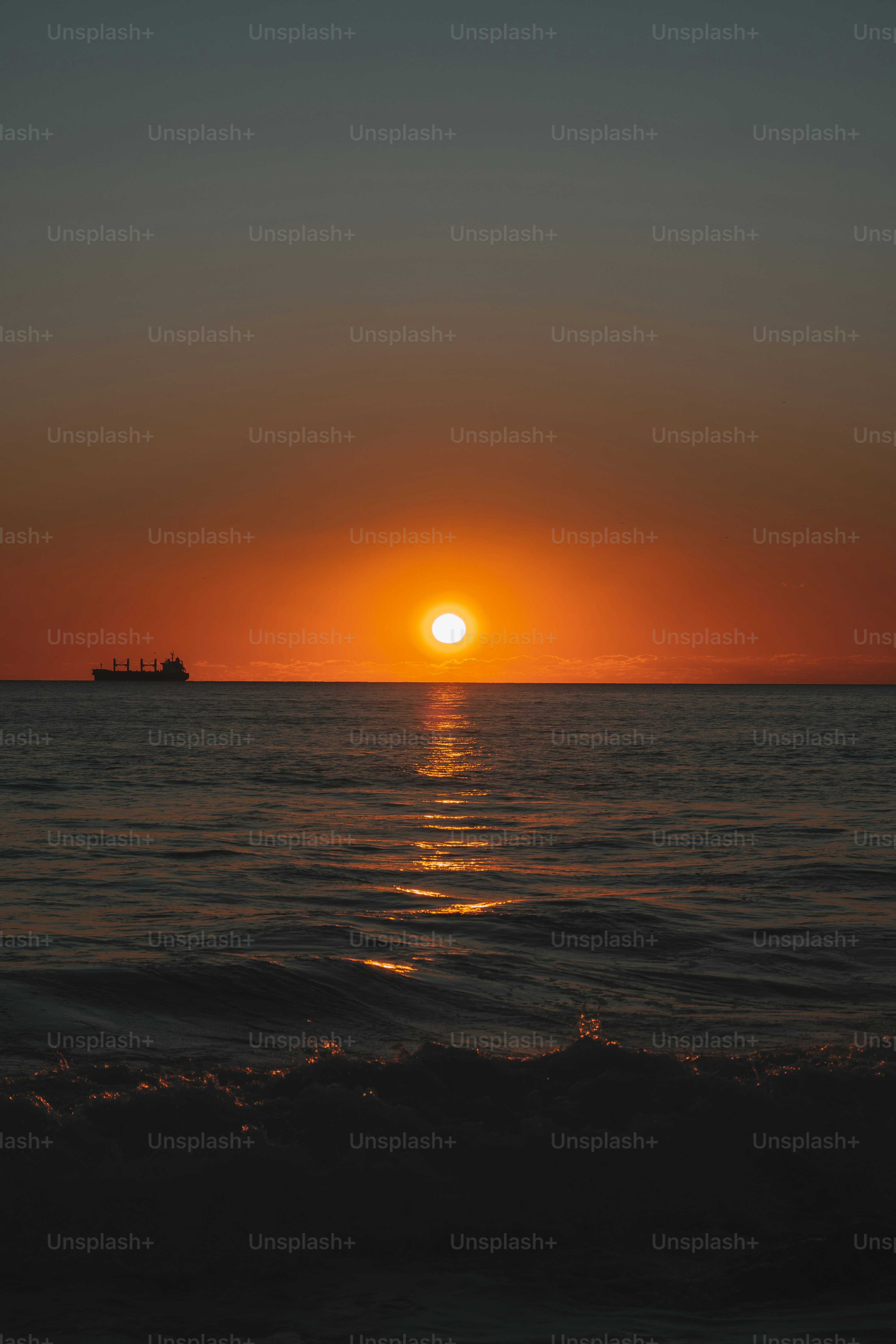 The sun is setting over the ocean with a boat in the distance photo ...