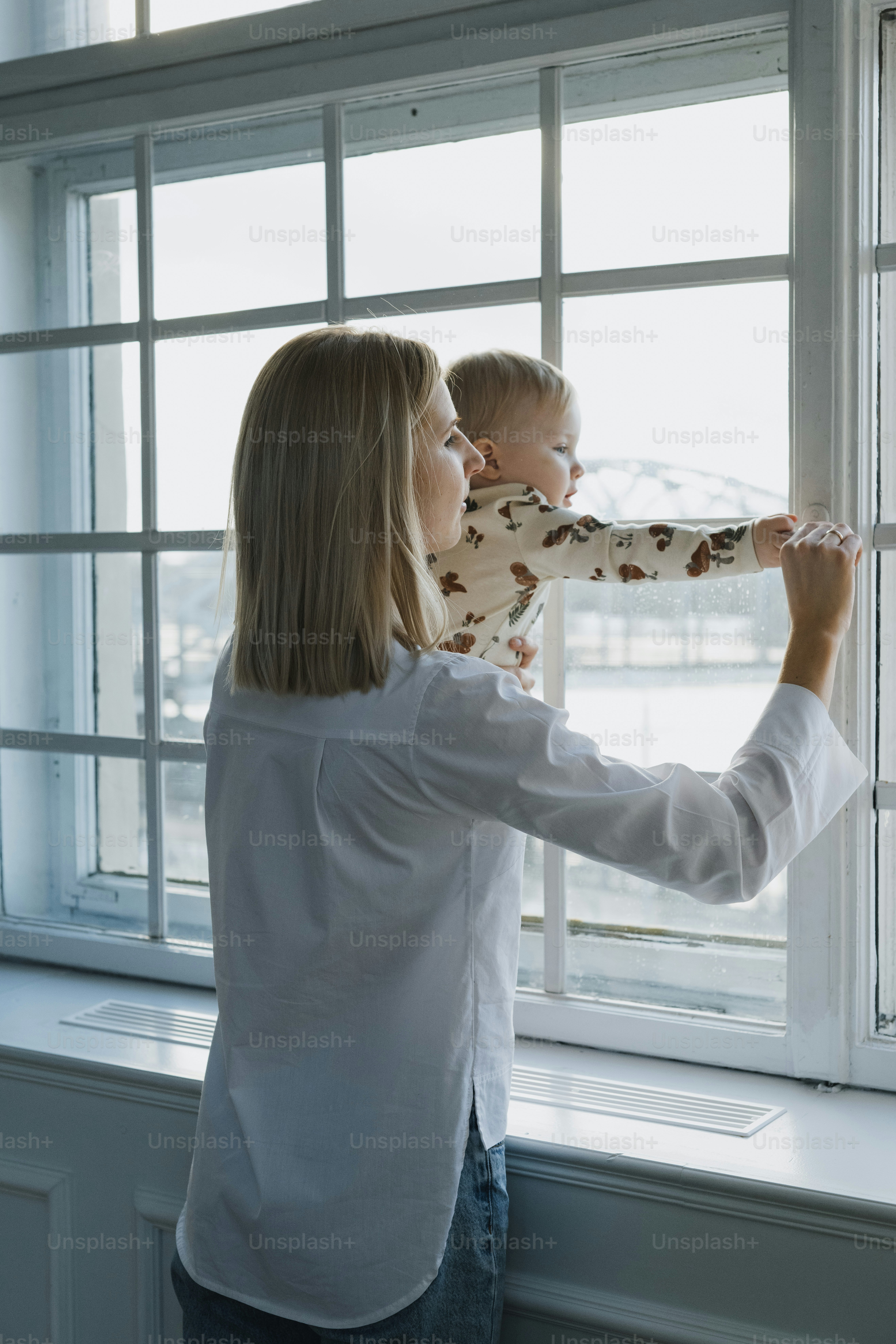 A woman holding a baby looking out of a window photo – Family Image on ...