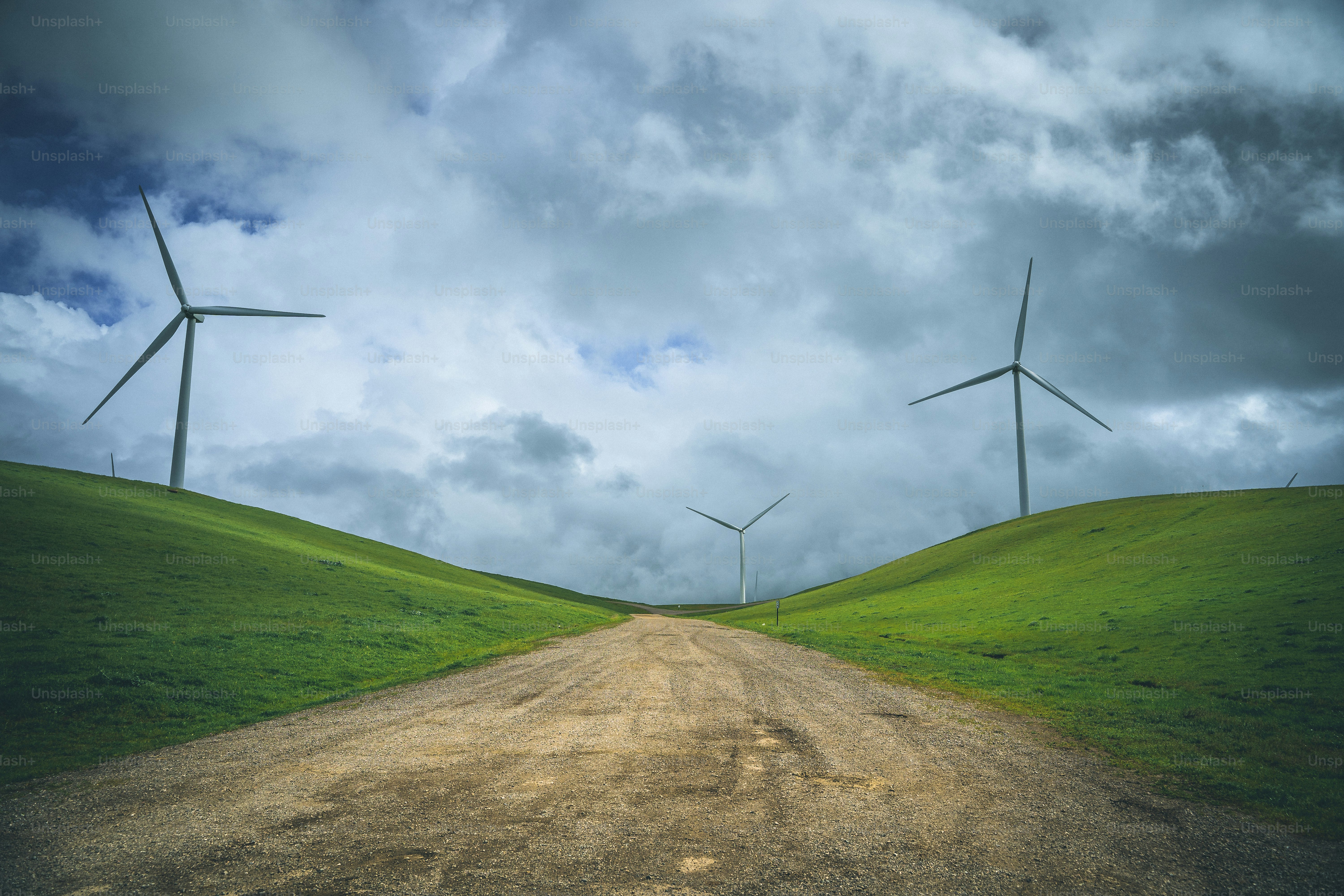 A dirt road with wind turbines in the background photo – Windmill Image ...