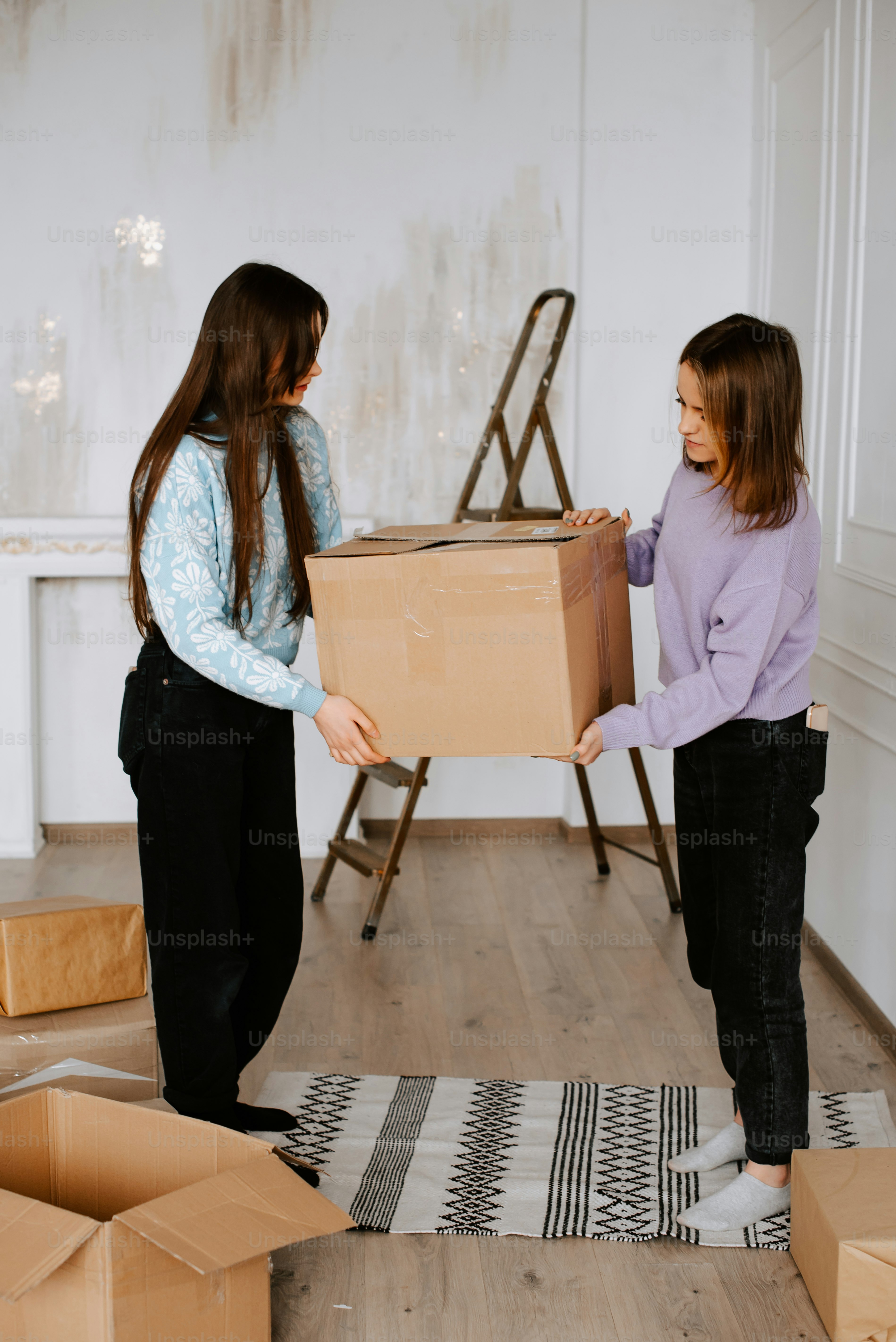 Two young women unpack boxes in a room photo – Packing boxes Image on ...