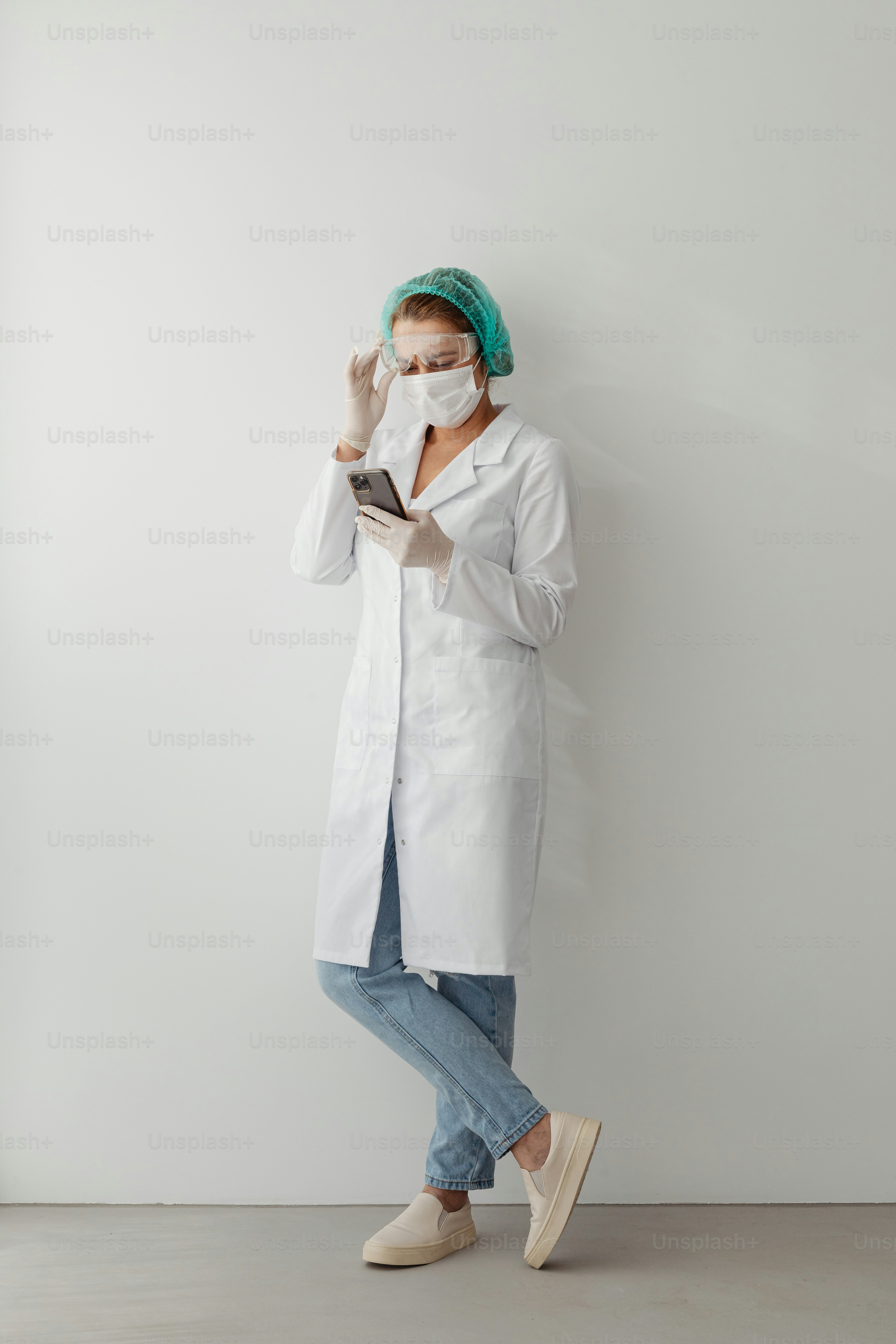 A woman wearing a white lab coat and mask photo – Looking at phone ...