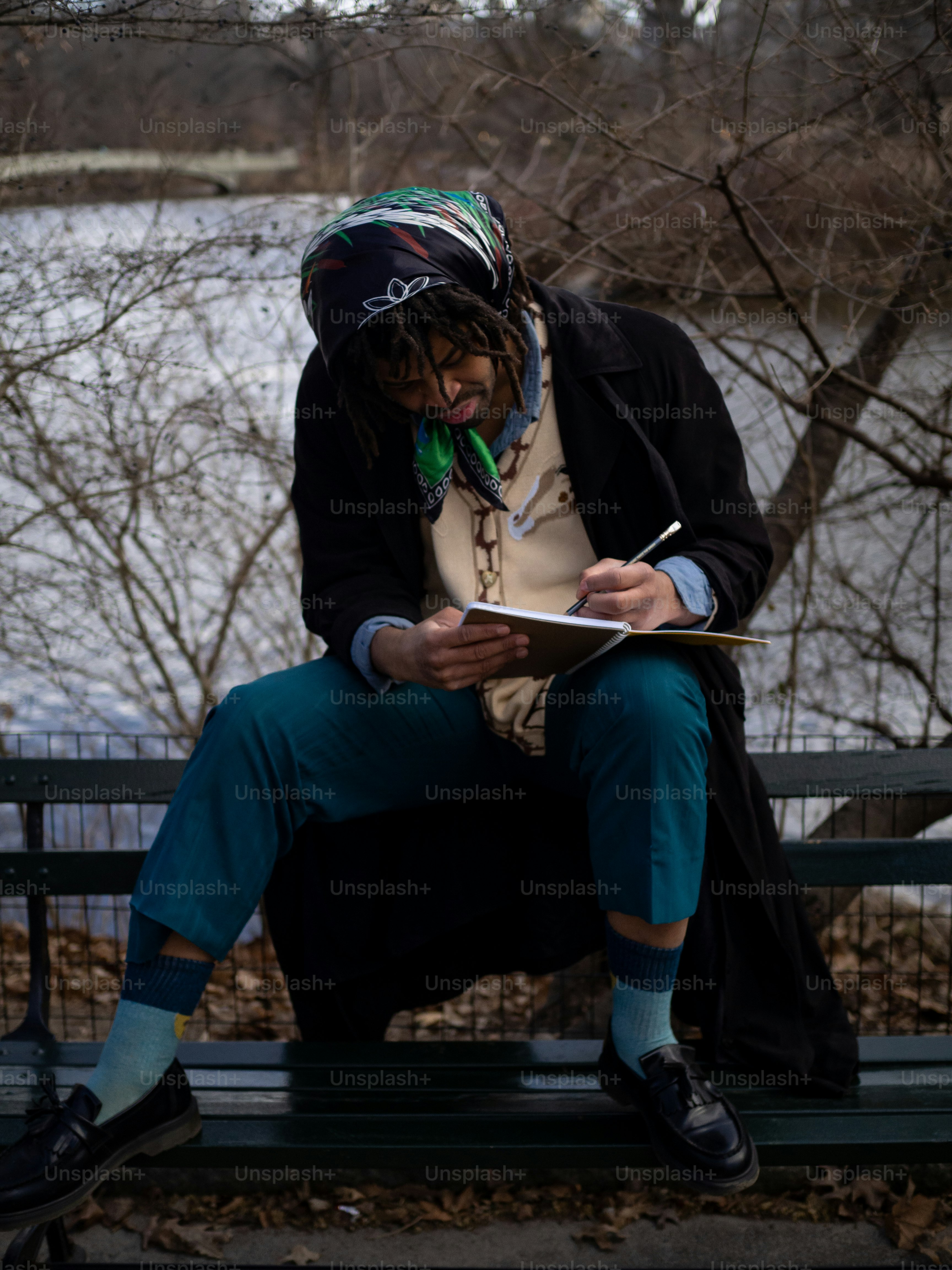 A person sitting on a bench writing on a notebook photo – Man Image on ...
