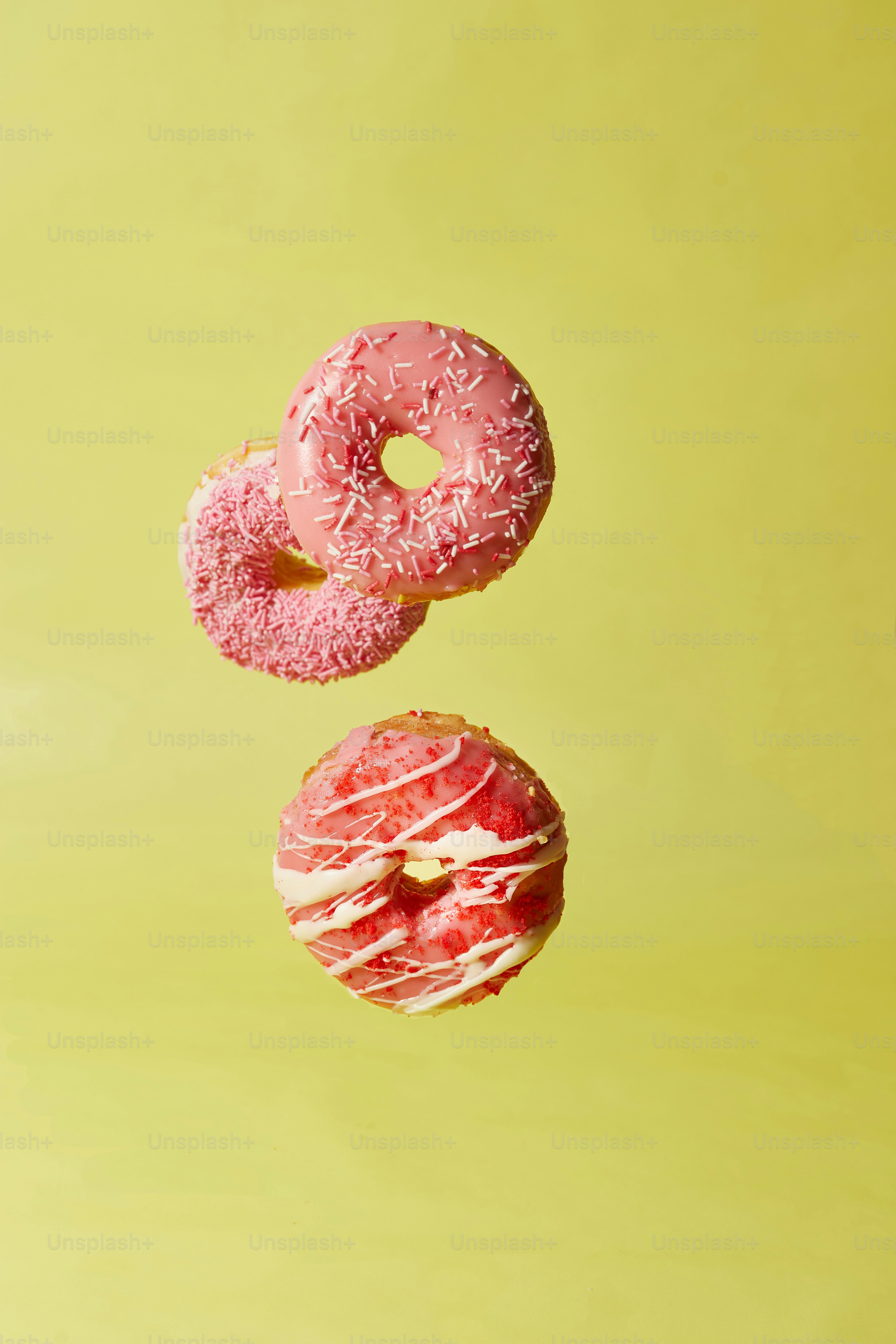 Three donuts with pink icing are flying in the air photo – Doughnuts ...