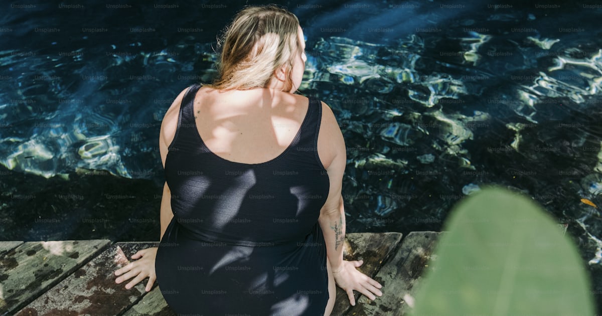 Foto zum Thema Eine Frau, die auf einem Dock sitzt und auf das Wasser ... Foto zum Thema Eine Frau, die auf einem Dock sitzt und auf das Wasser ...