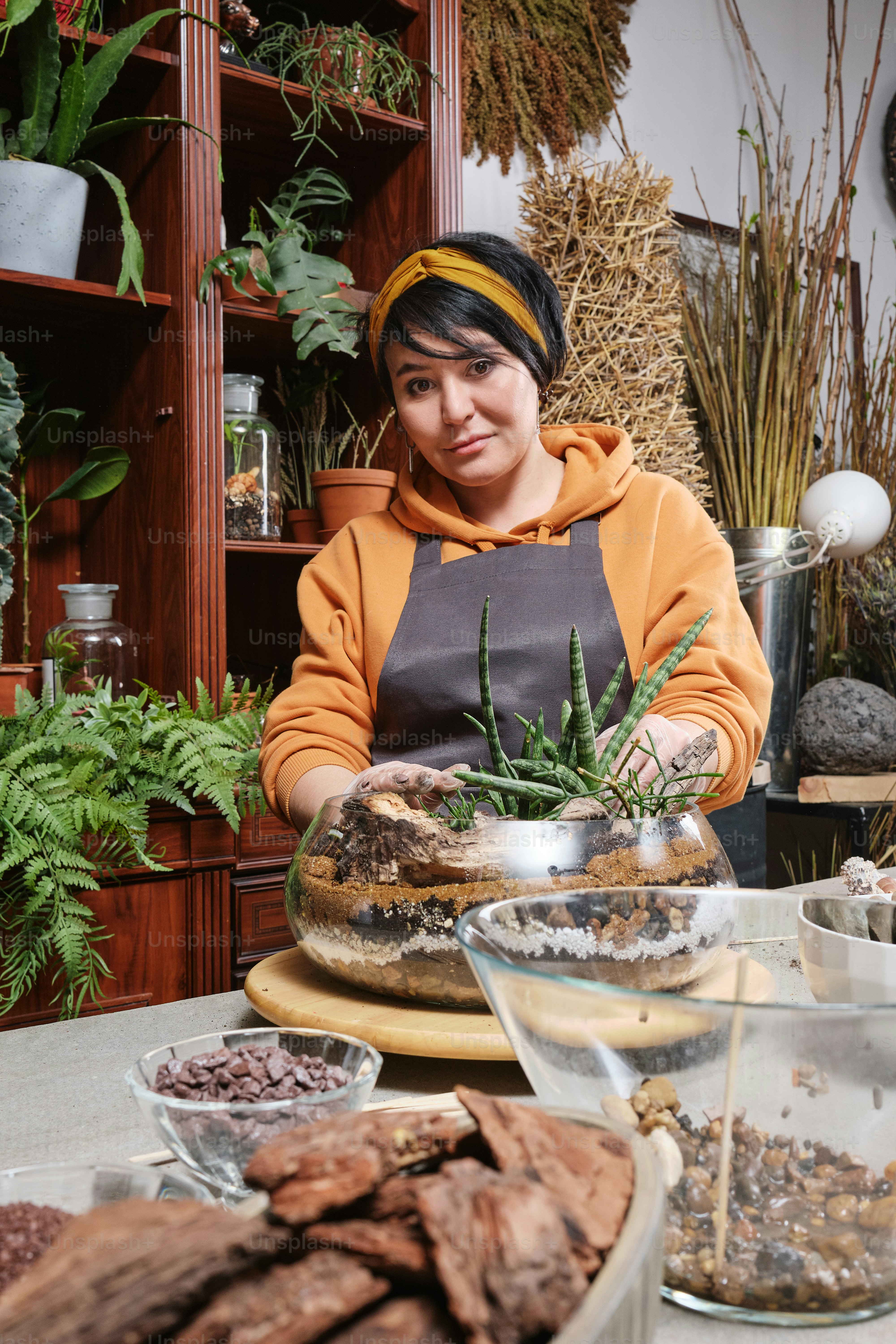 A woman standing behind a table filled with plants photo – Small ...