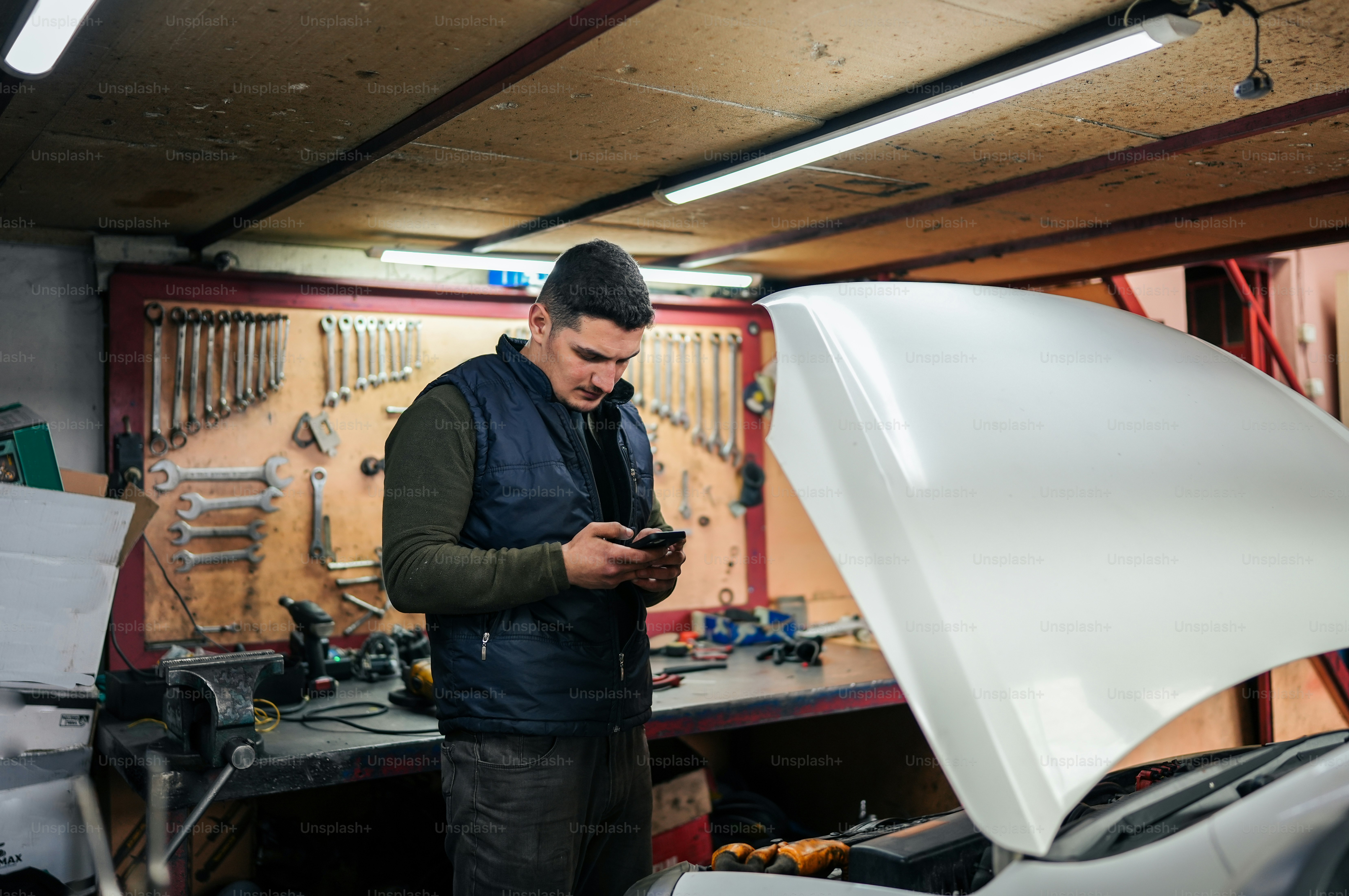 A man in a garage looking at his cell phone photo – Car Image on Unsplash